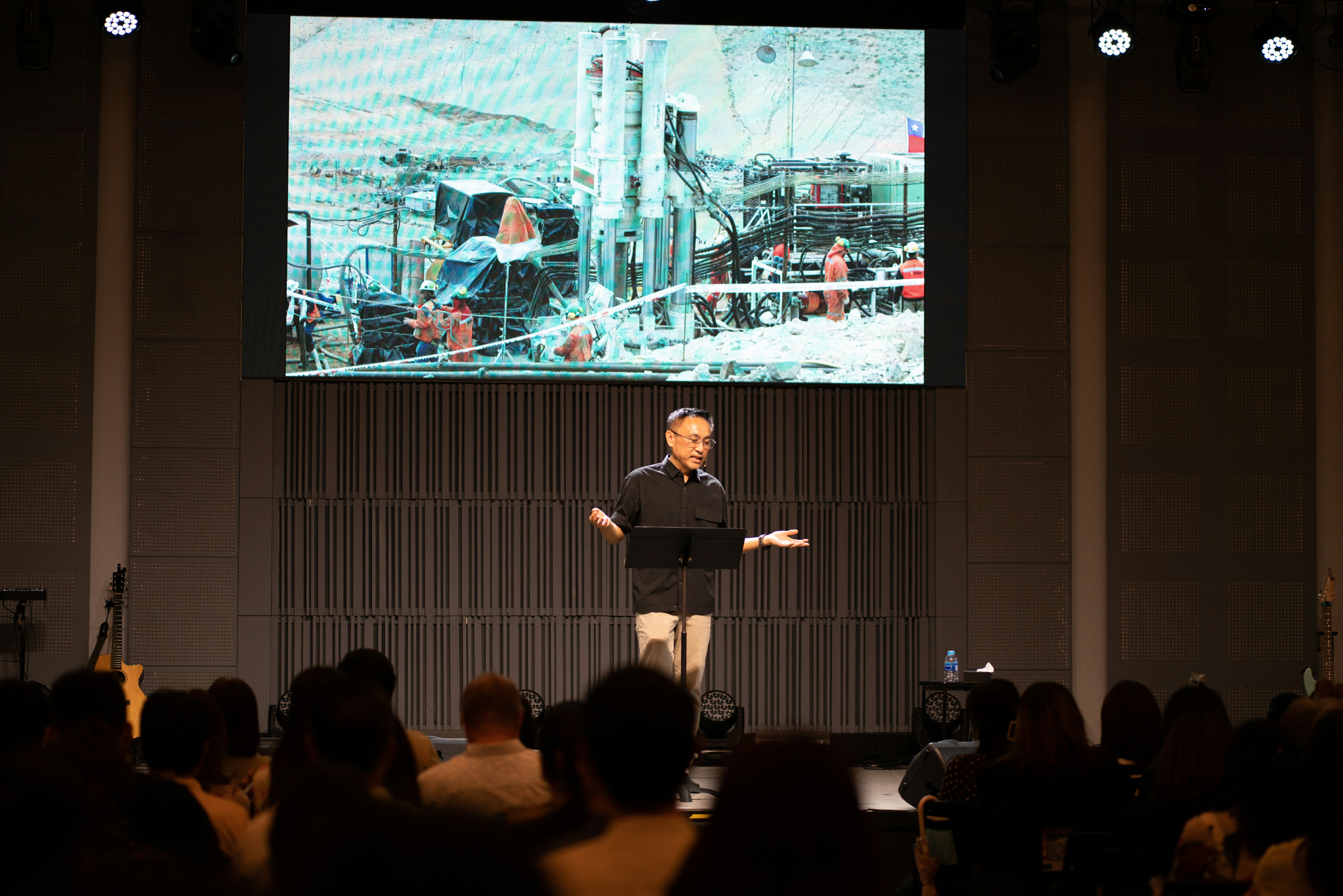 Speaker on stage with large LED screen presenting industrial scene