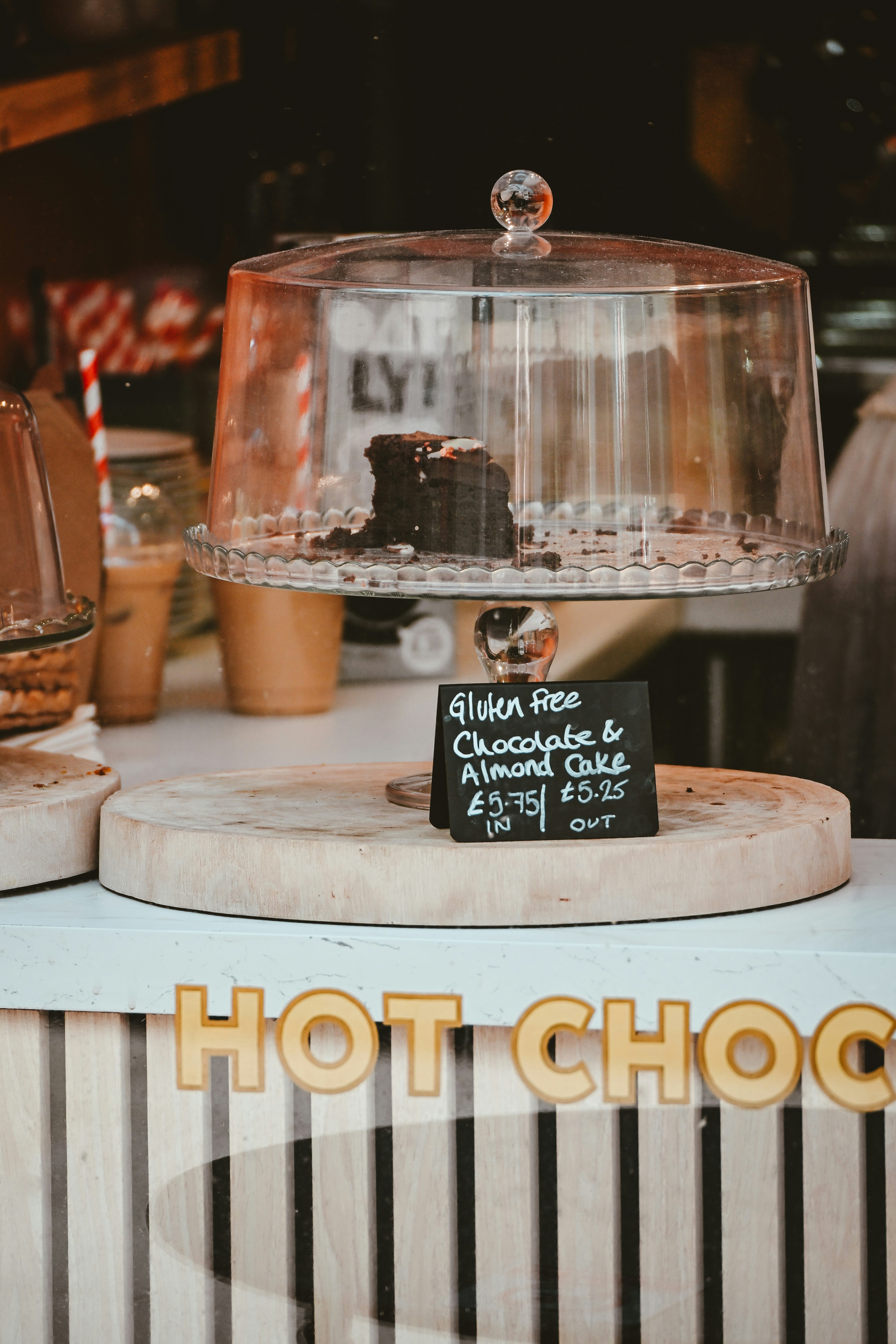 Glass cake dome on a wooden pedestal guarding a gluten-free chocolate & almond cake
