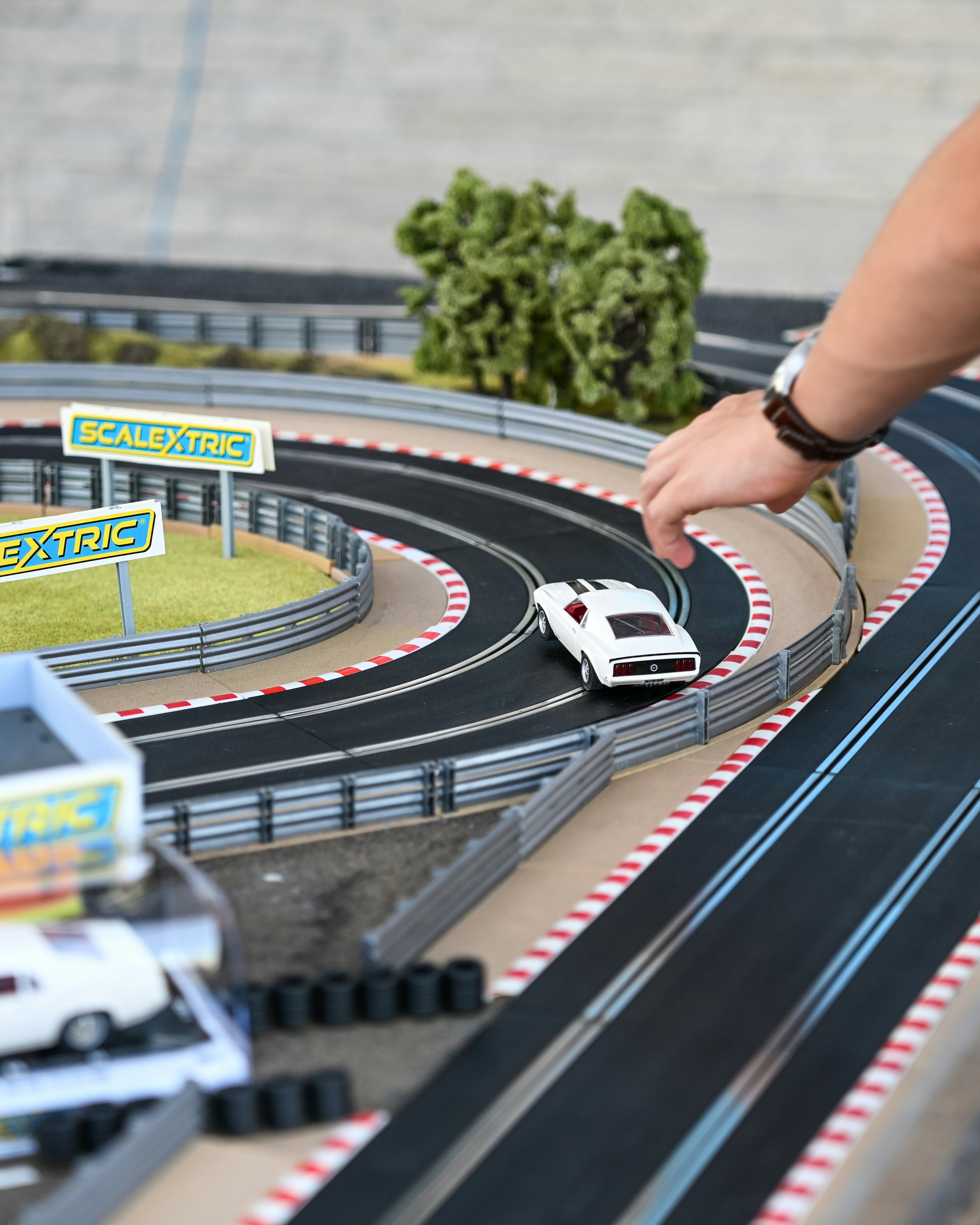 Hand-Driven Race: A Tiny White Hero Navigates a Scenic Slot-Car Track