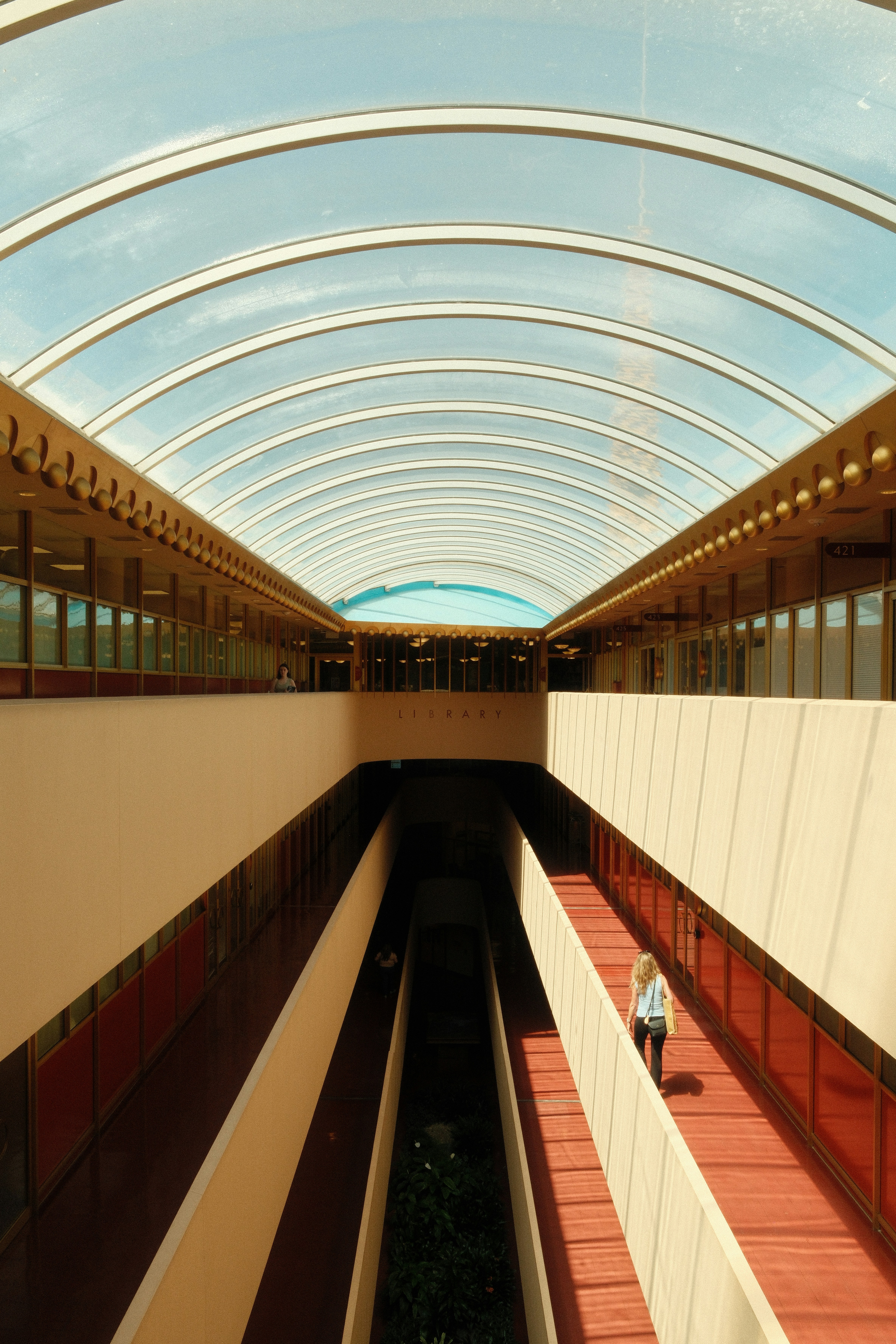 Architectural Skywalk: A Lone Visitor on the Red-Toned Corridor
