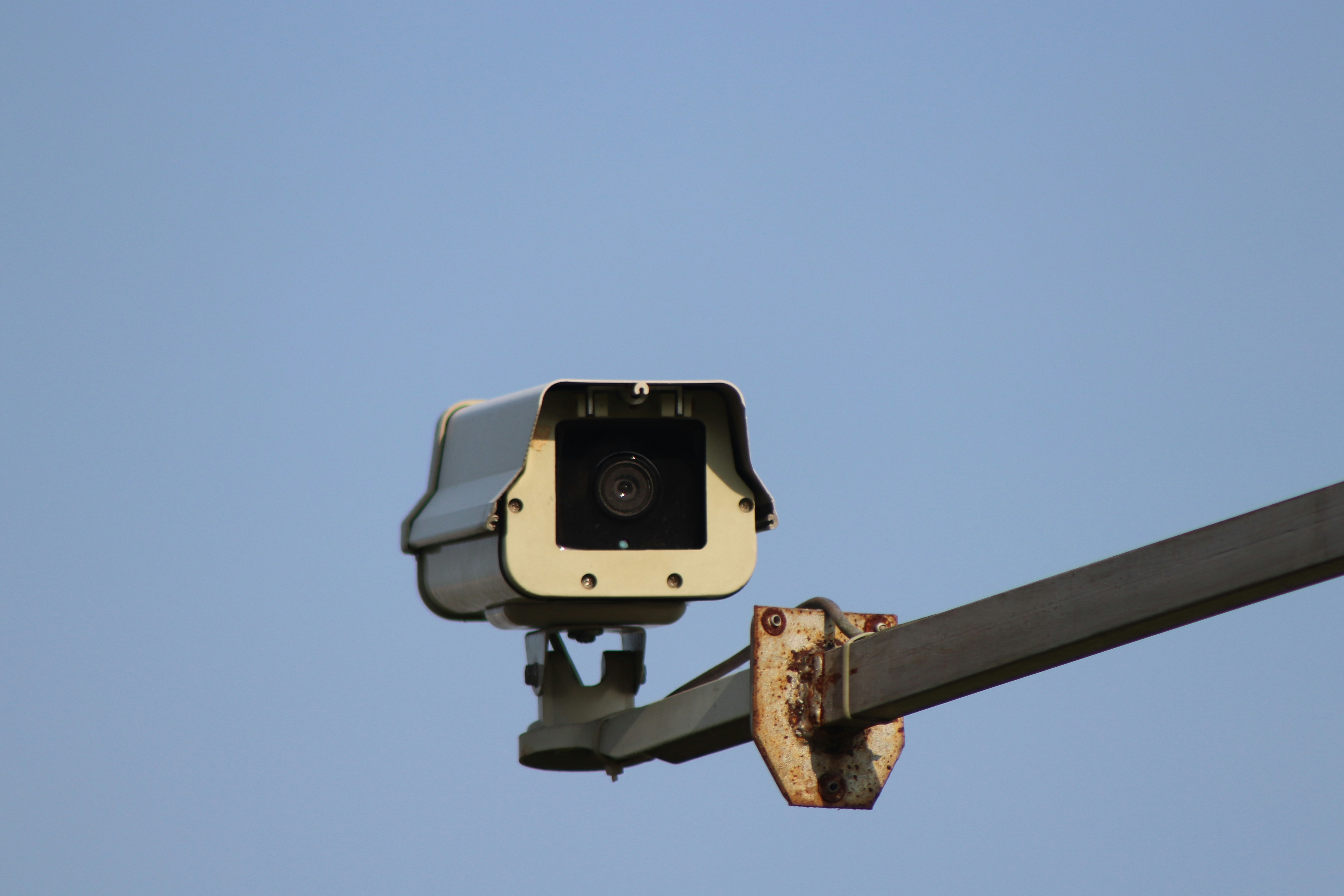 Sentinel on a Rusted Arm: A Close-up of a Surveillance Eye Against a Clear Sky