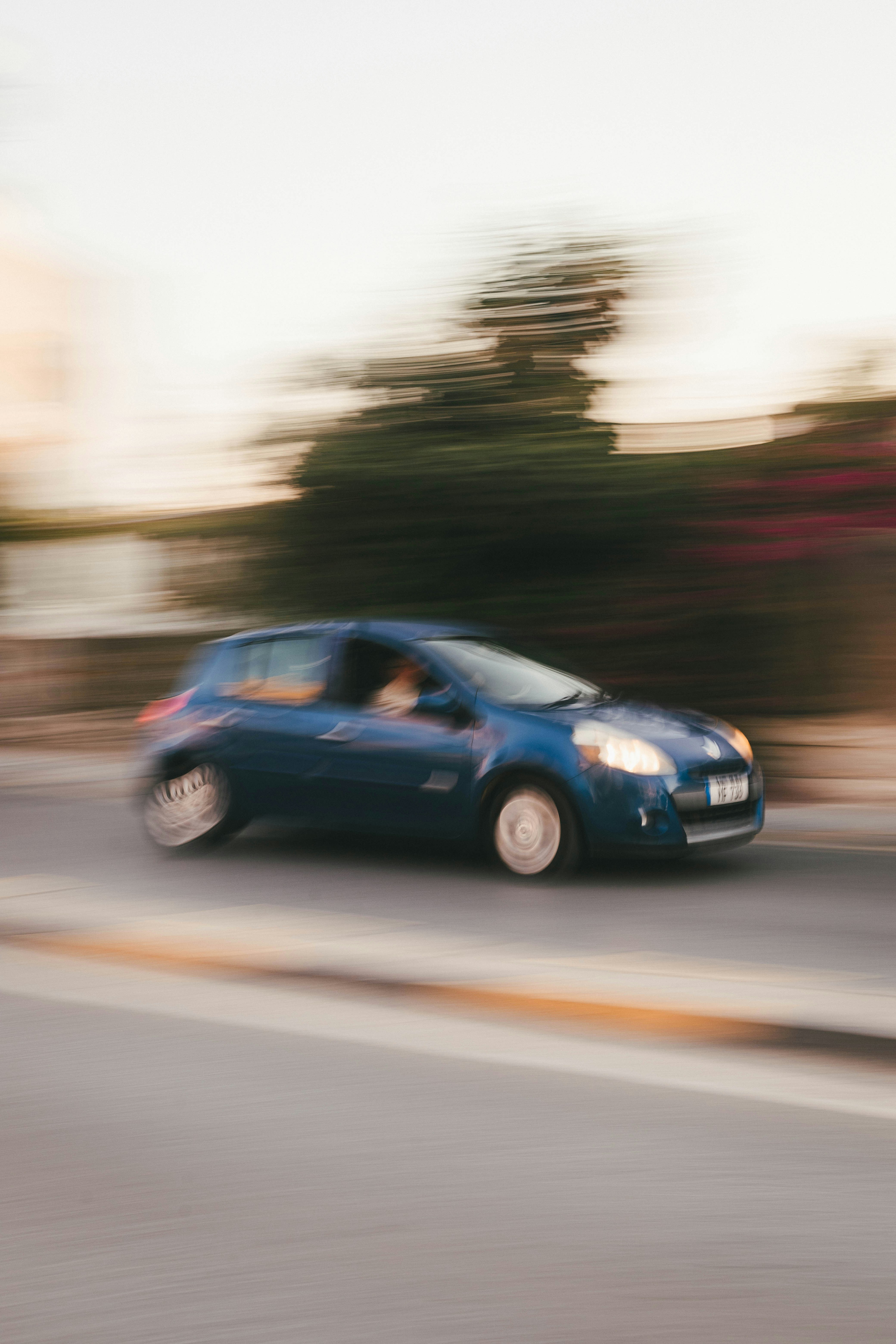 Blue car in motion blur along a sunlit street