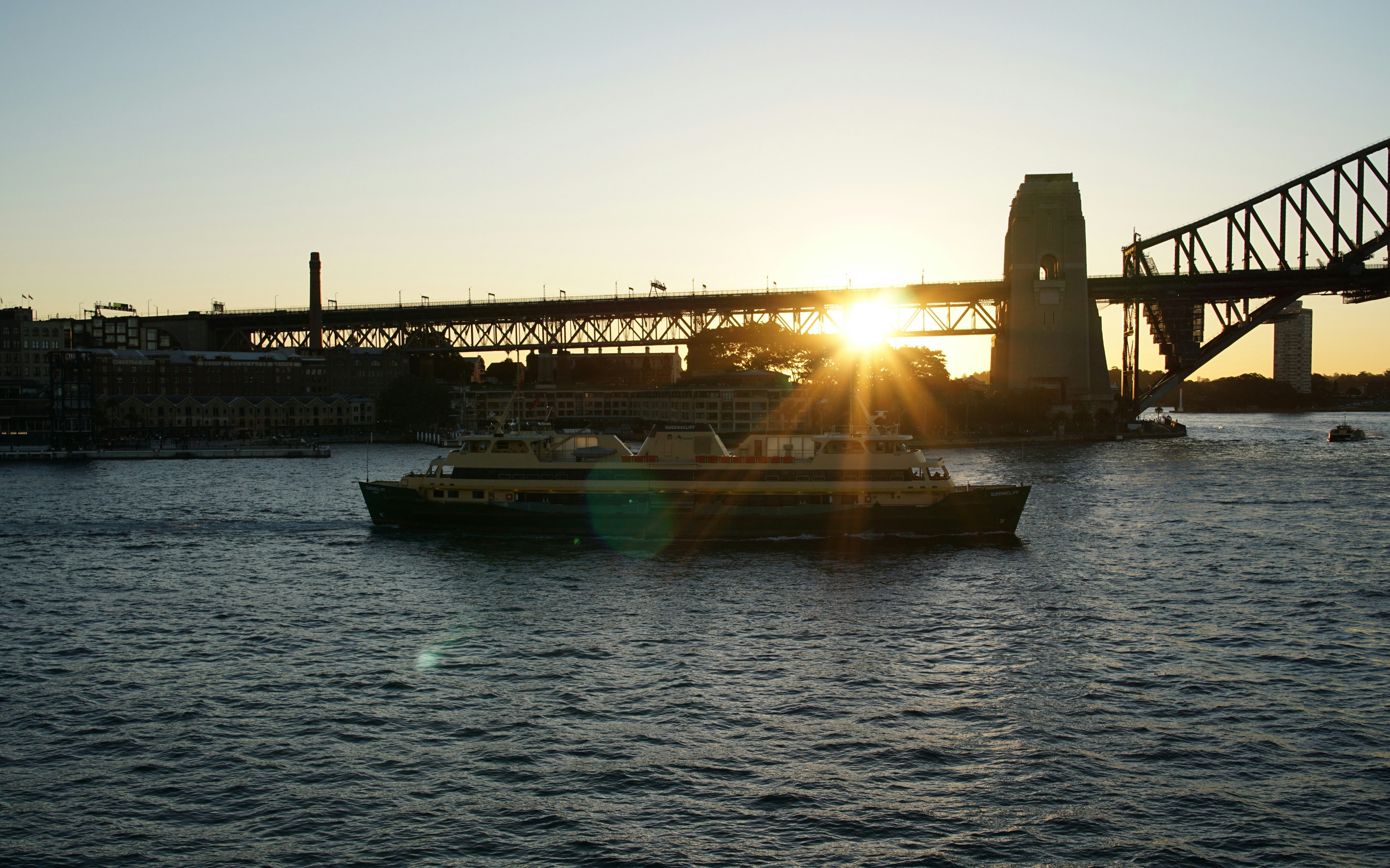 Sunlit Ferry under the Iron Arch: A City at Dusk