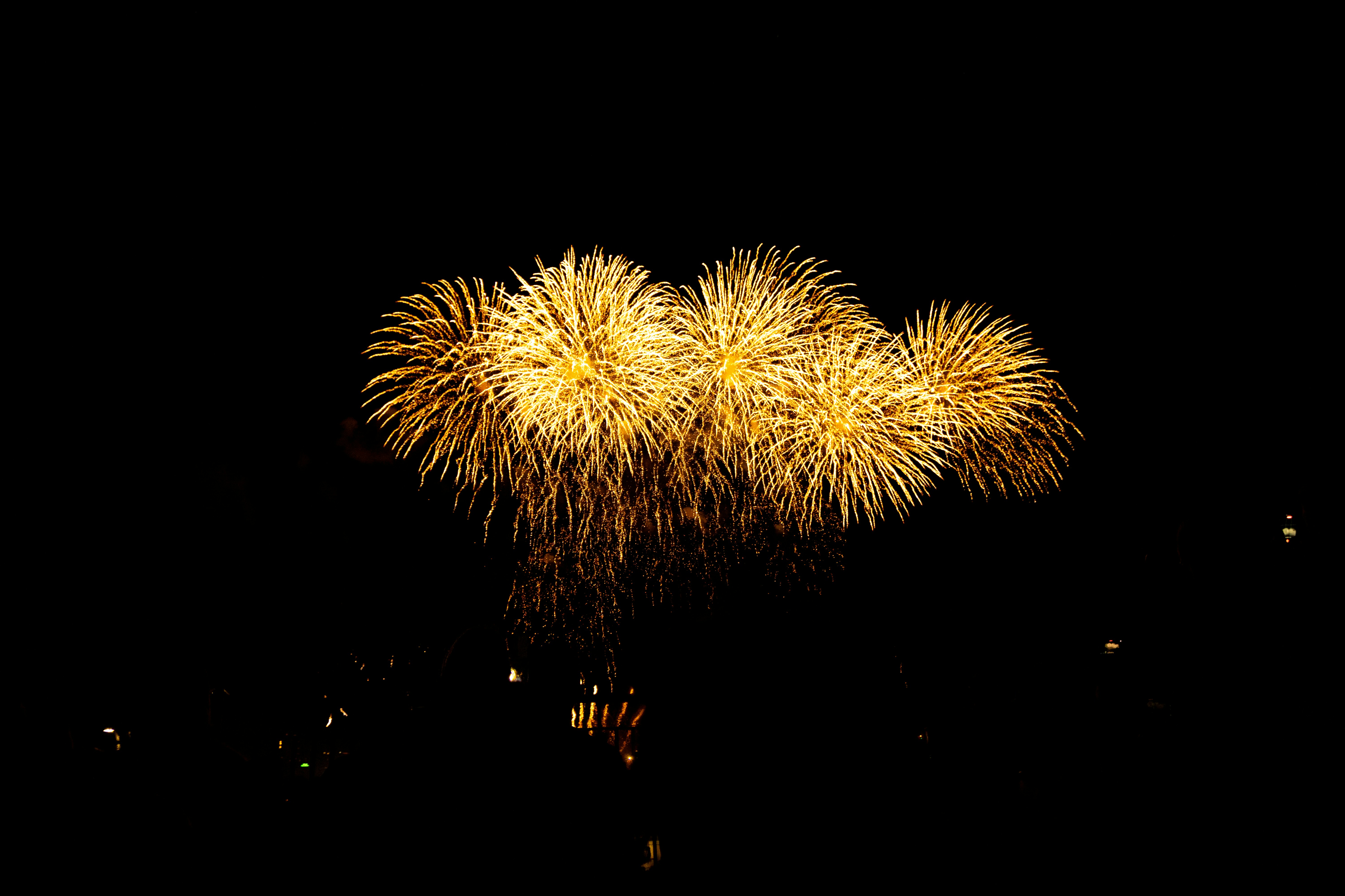 Golden fireworks erupt above a dark cityscape, illuminating the night sky with a warm, festive glow.