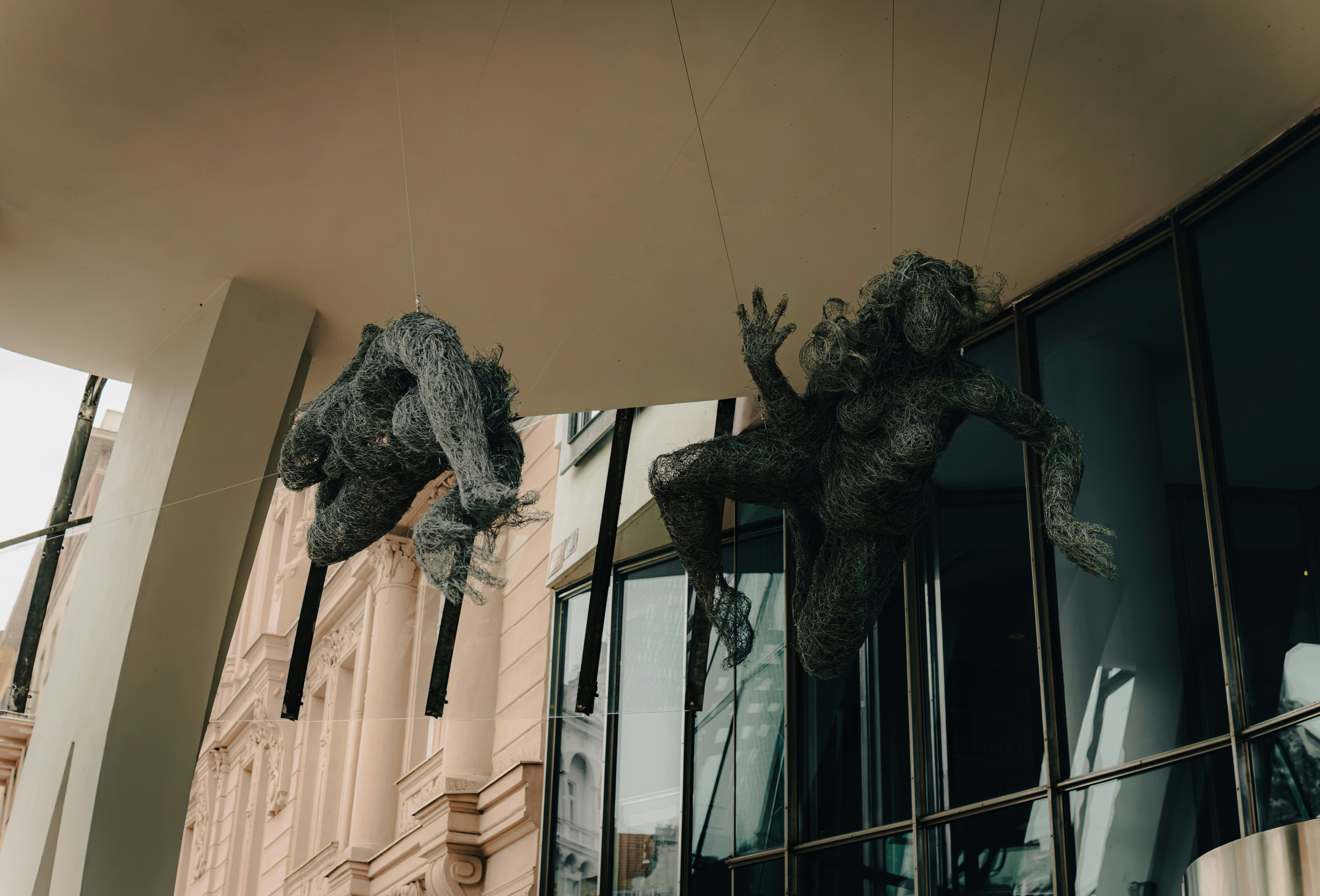 Suspended Figures: Ghostly Sculptures Hover Over a Glass Facade