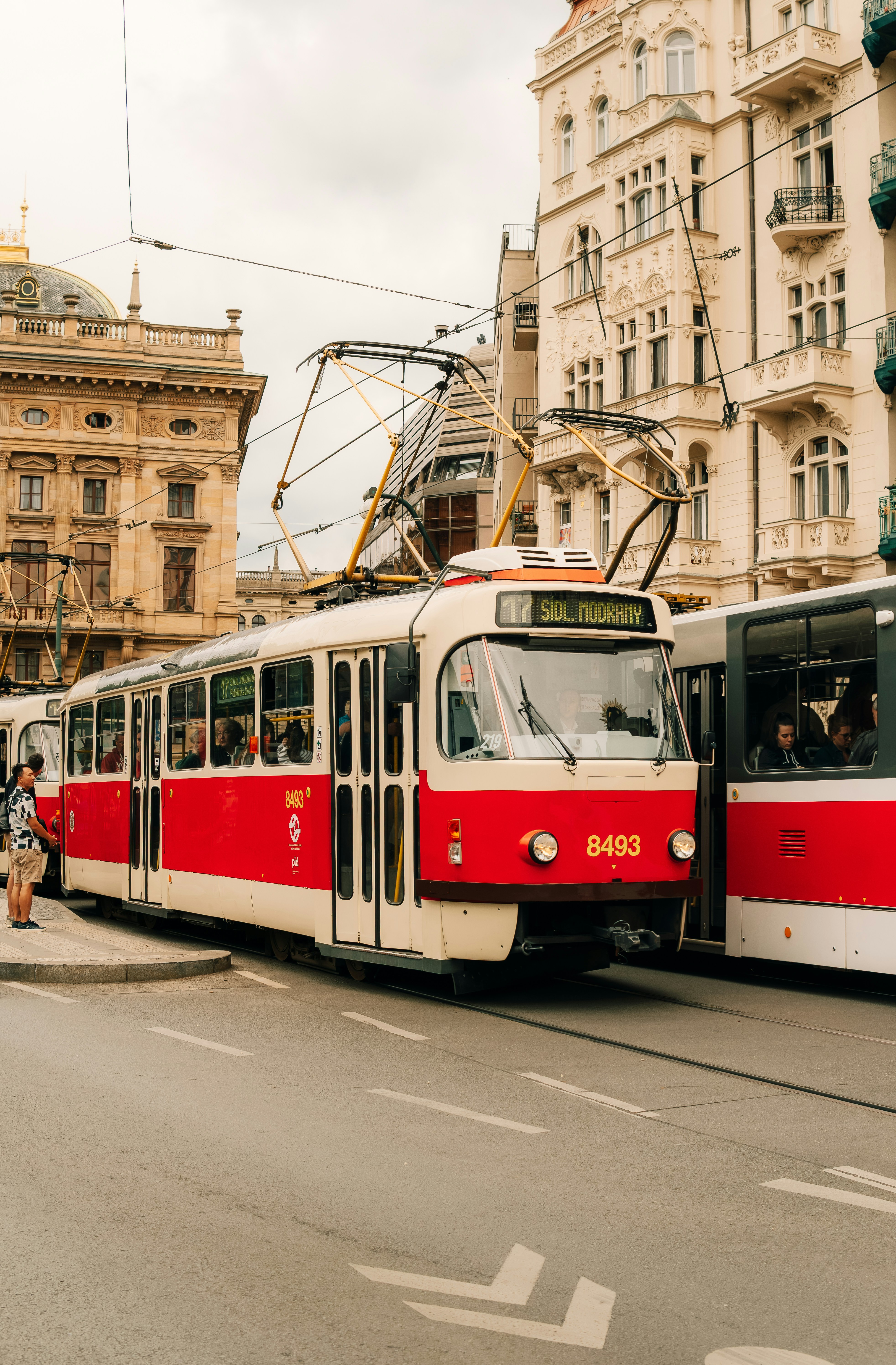 A red-and-white tram glides along a city street with ornate buildings in the background, capturing everyday urban transit. This is a photographic scene, not a painting or illustration.