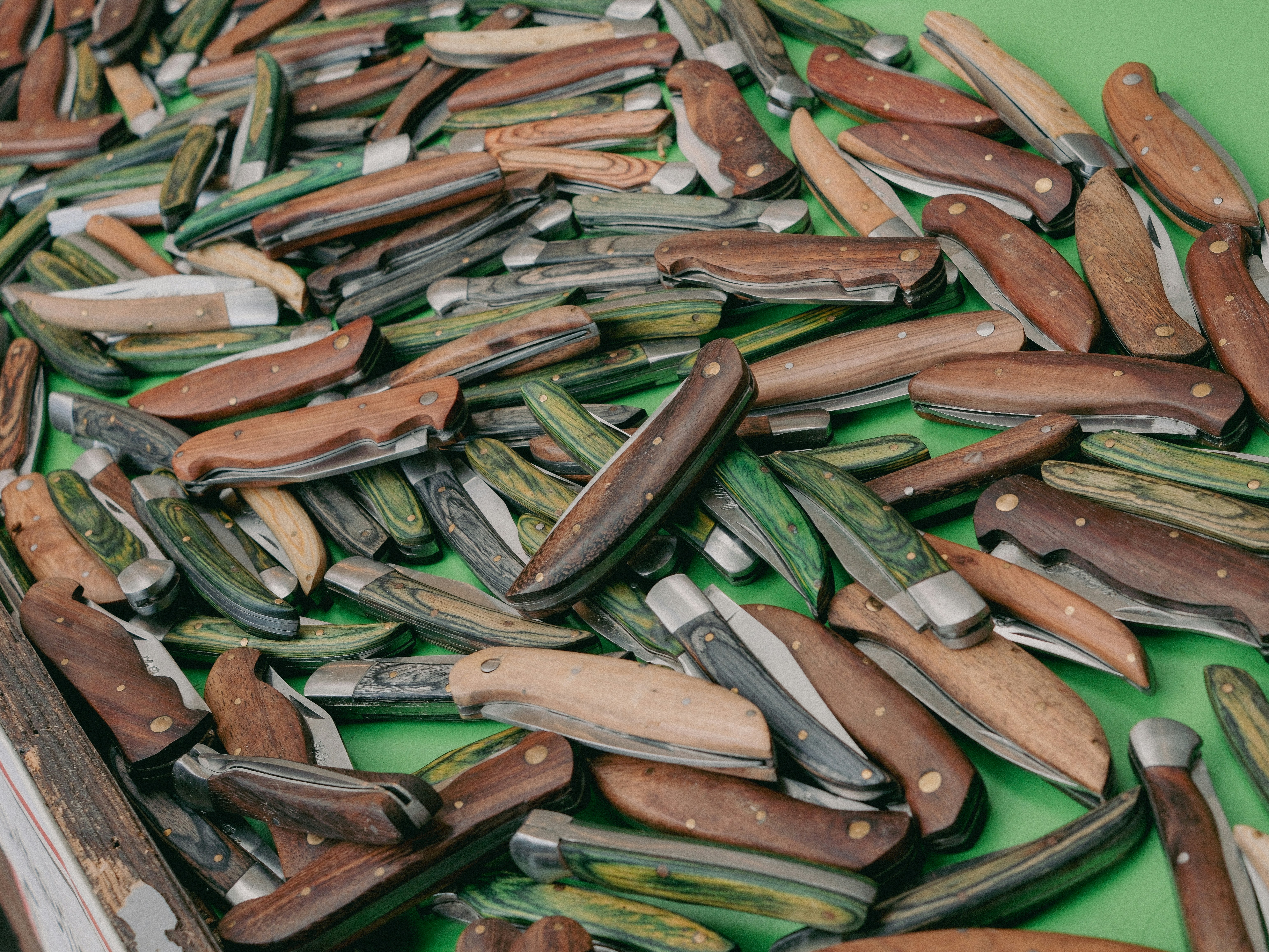 Assortment of folded wooden pocket knives scattered across a green background