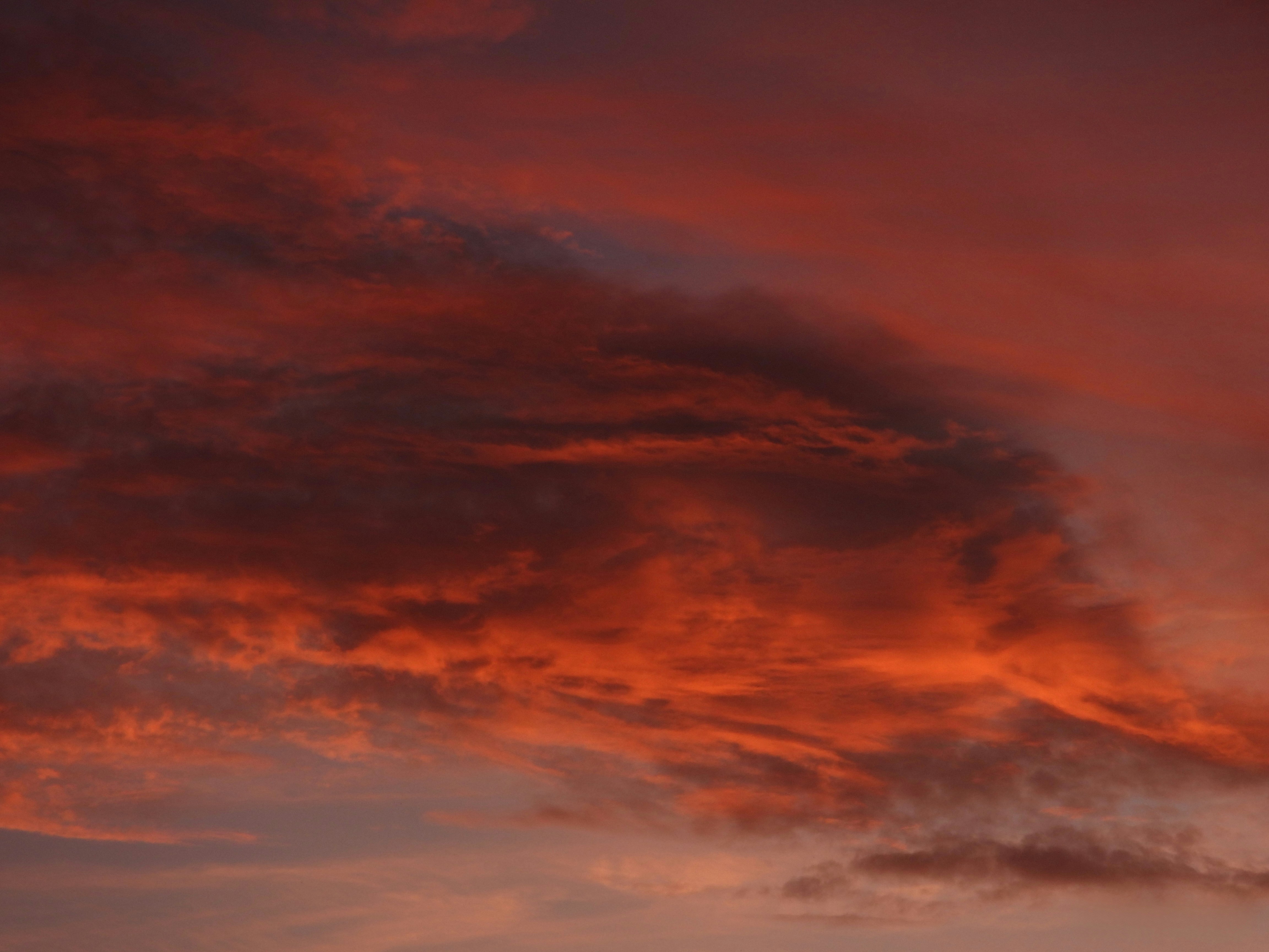 Vibrant sunset clouds blaze in crimson over a tranquil horizon, emphasizing dramatic color and texture. Note: a landscape sky scene.