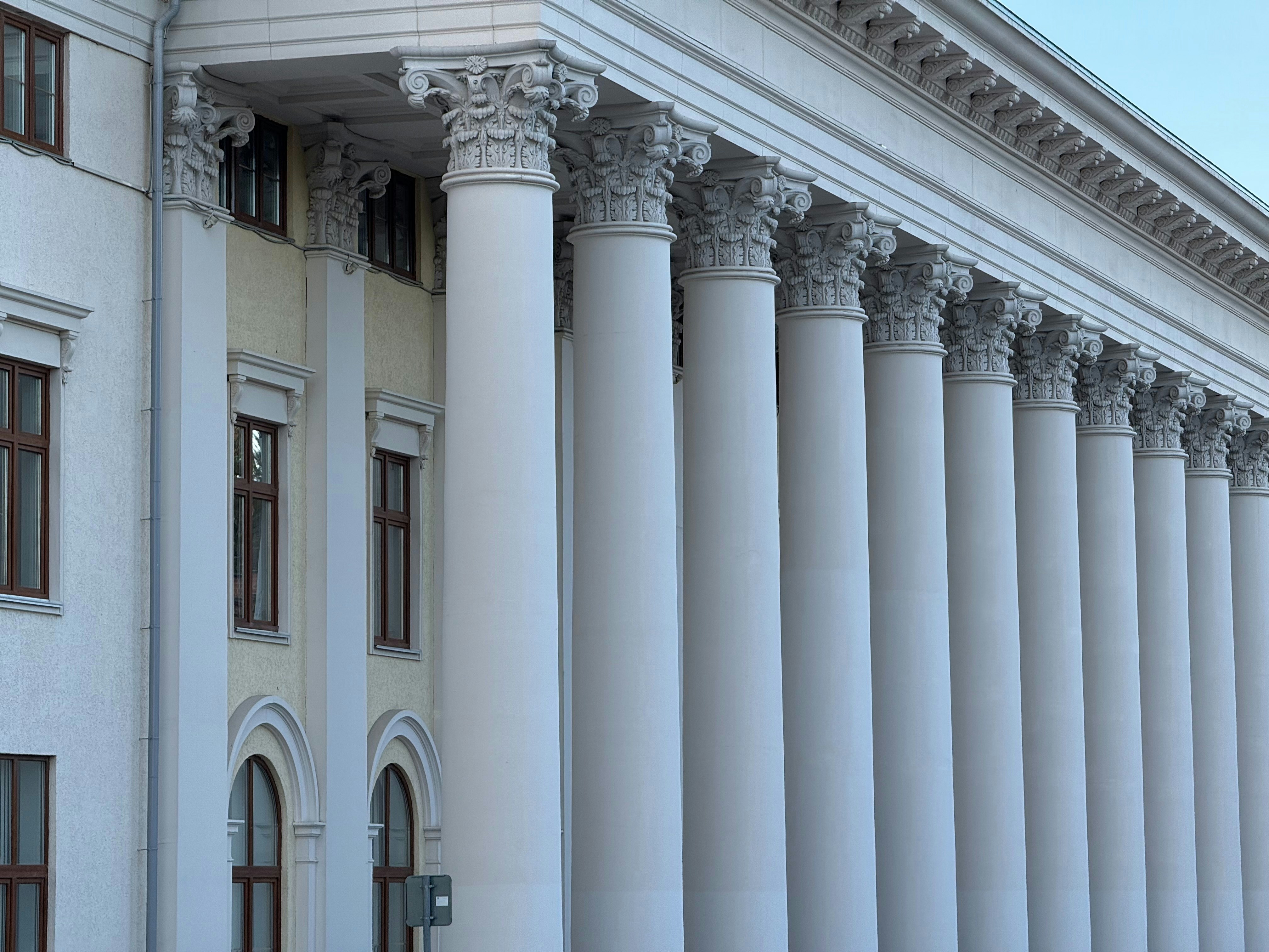 A grand colonnade with tall white columns and classical details, captured in soft daylight. Architectural depth and rhythm emphasize the building's historic façade.