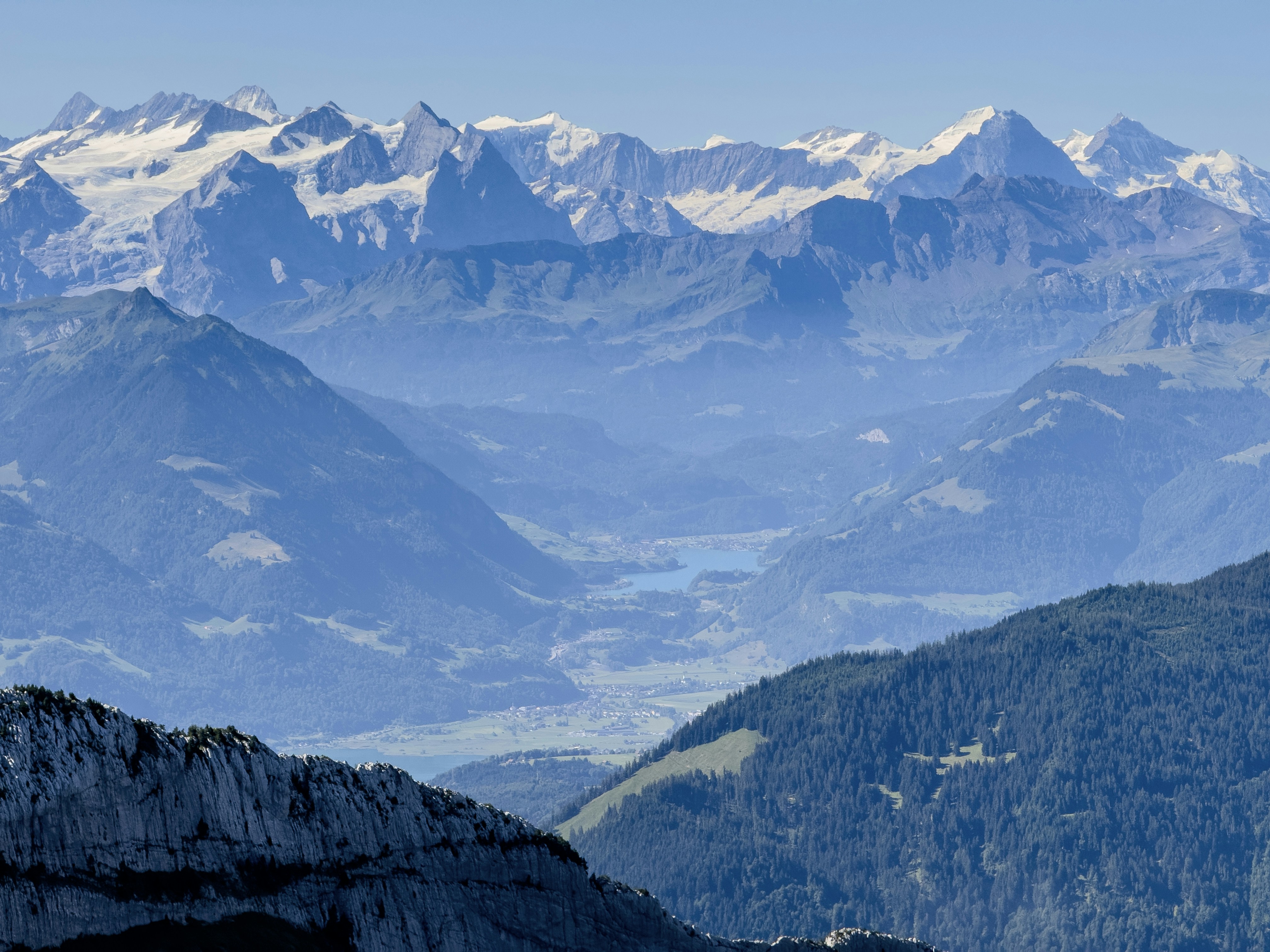 Mountain valley panorama with snow-capped peaks and layered blue mist; foreground ridges lead toward distant valley, showcasing depth and atmosphere. (Landscape photograph).