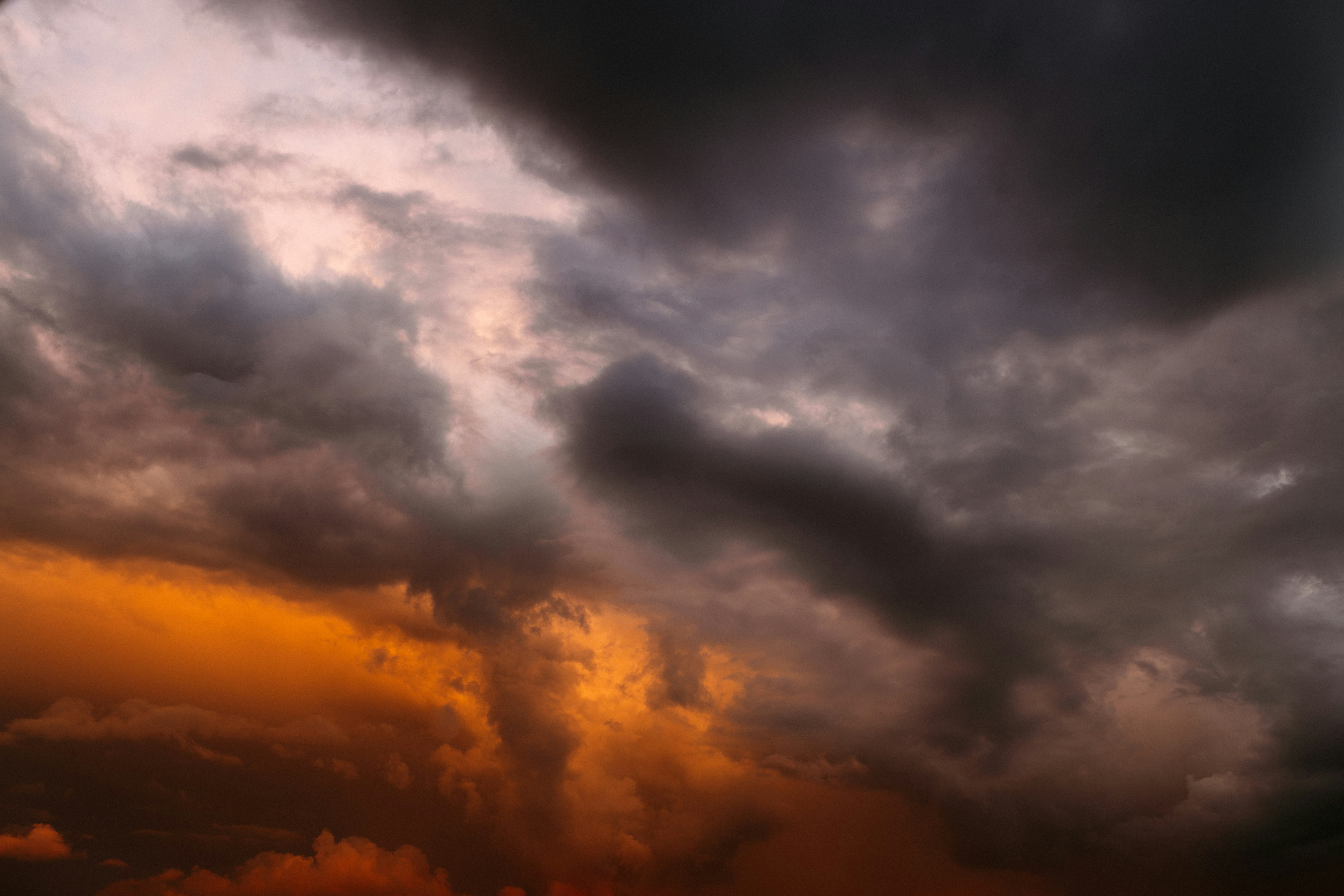 Dramatic storm clouds blaze with orange undertones as sun-filtered light spills through the lower left, creating a moody, high-contrast sky. The image captures an atmospheric, painterly moment of sunset or storm light.