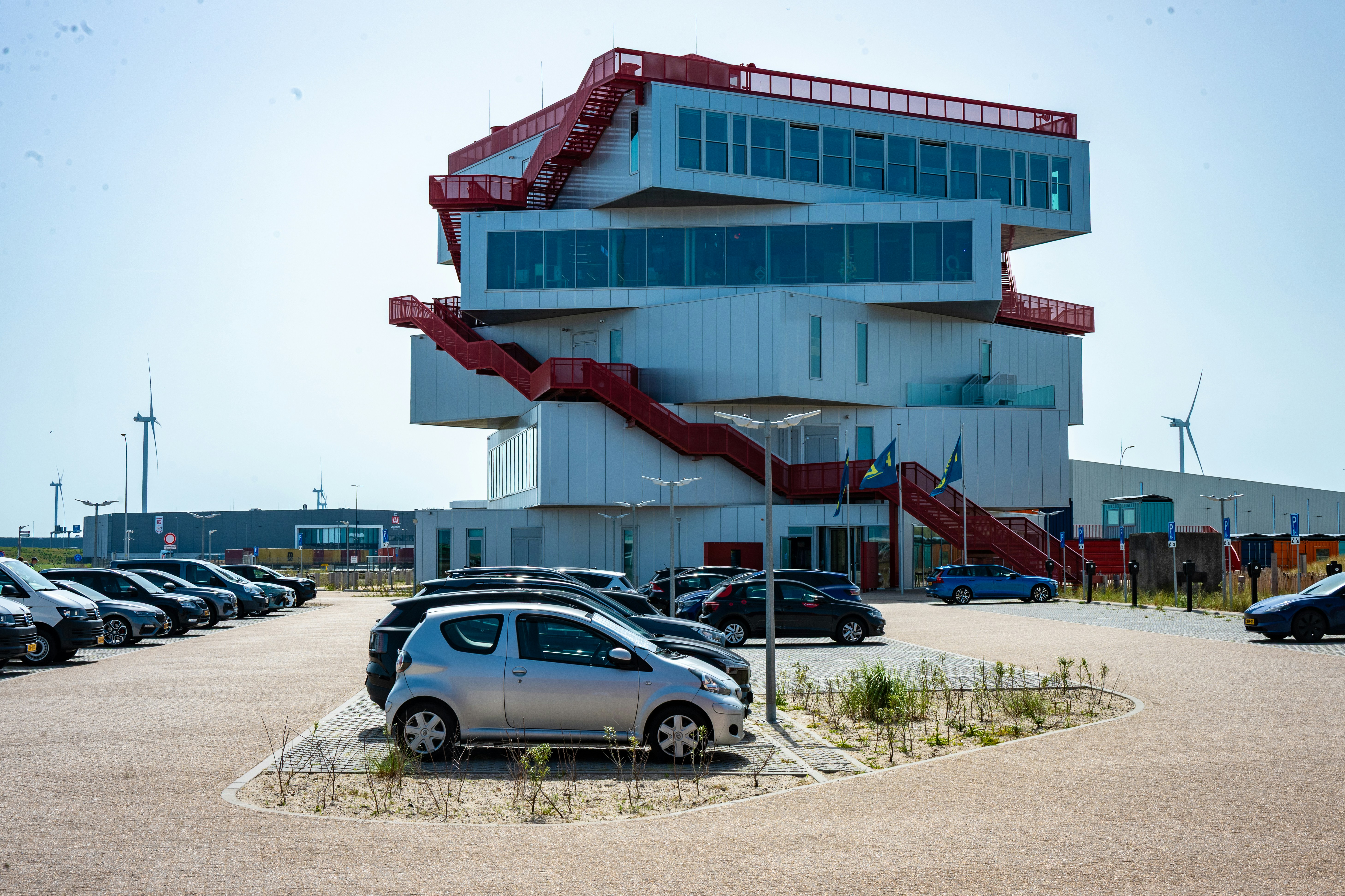 Astride the Wind: Modern Red Staircase Tower Over a Car-Yard Clearing