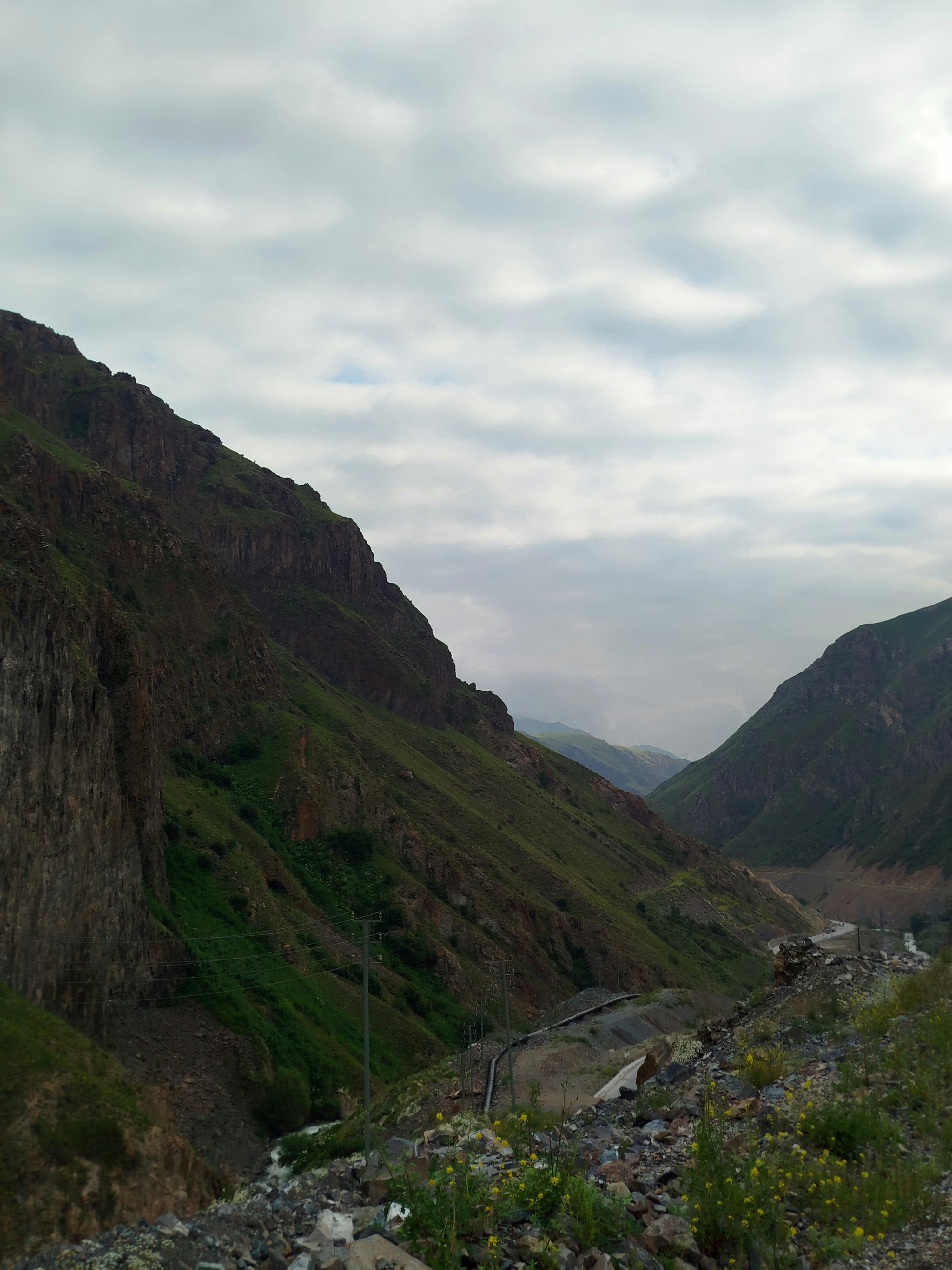 Rugged mountain gorge with a winding road and rocky foreground beneath a cloudy sky.