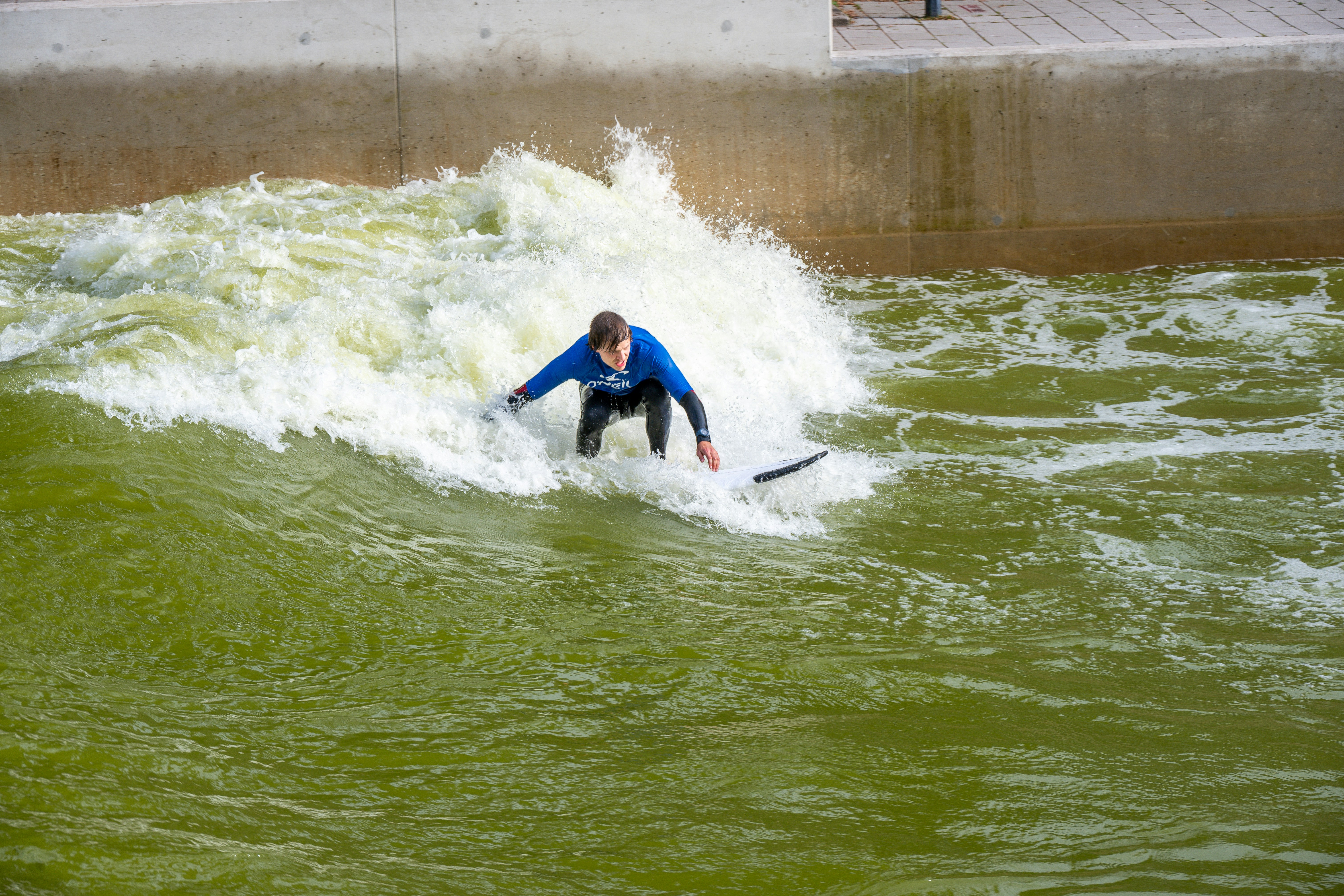 Blue-Suited Surfer Carving a Green Wall at a Concrete Channel