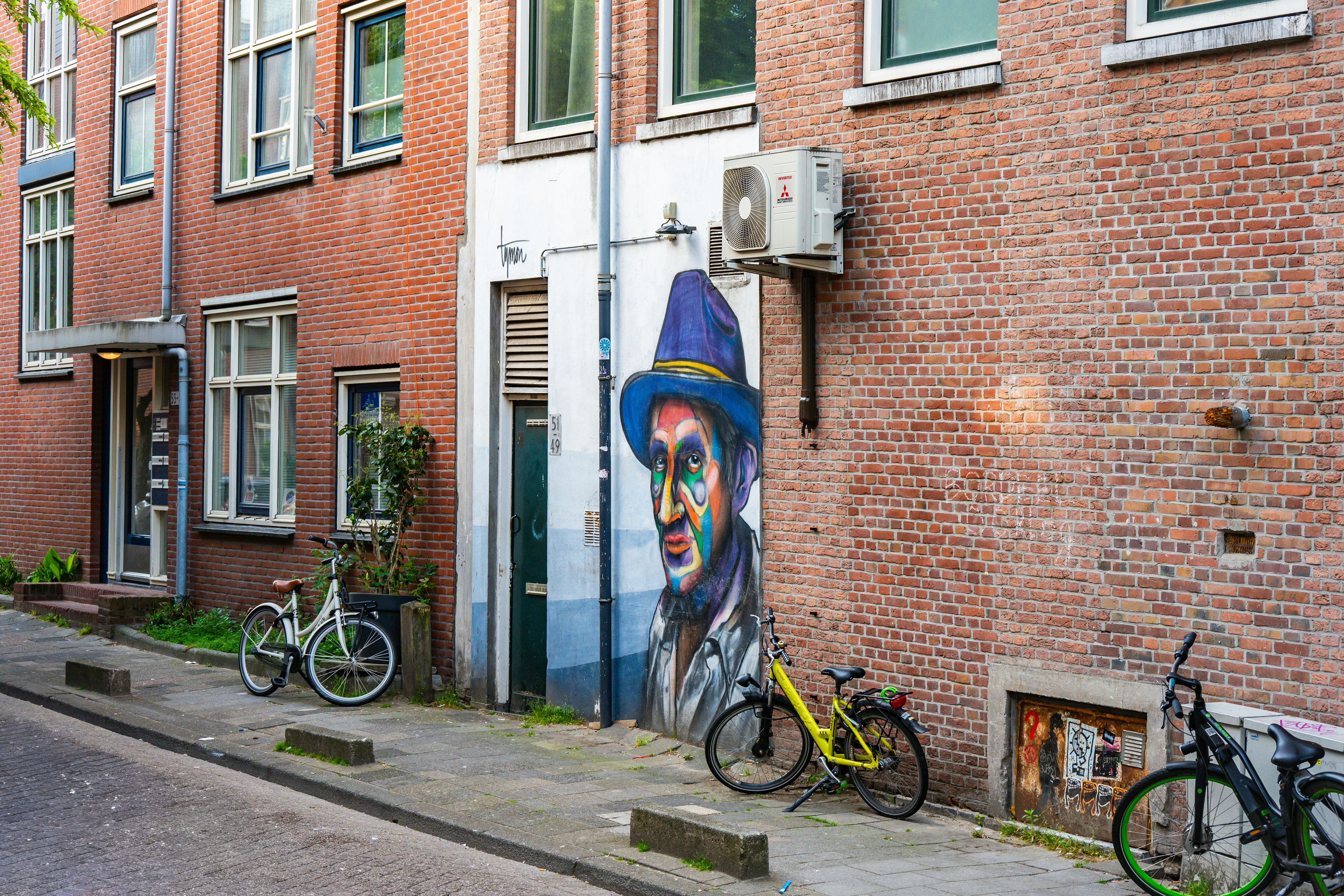 Mural maestro by the bike rack: a blue-hatted portrait on brick streets