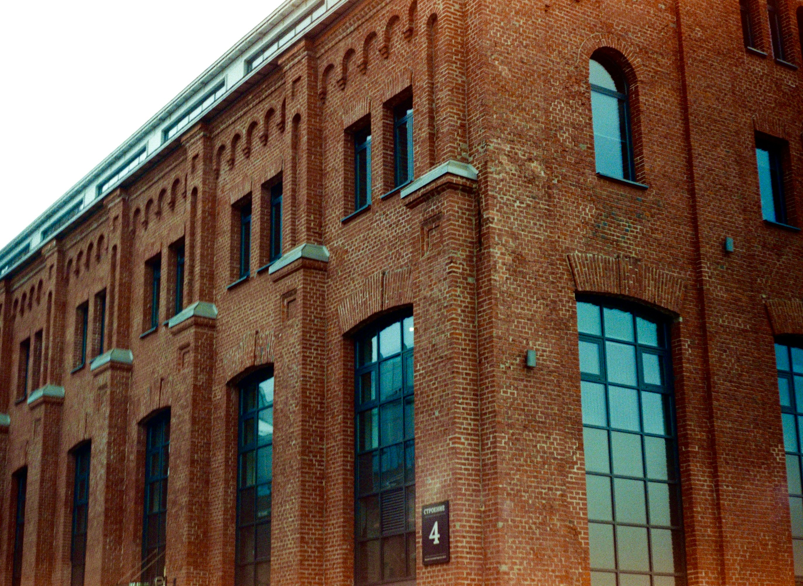 Red brick factory building with tall arched windows and a corner entry, capturing the architectural rhythm and industrial charm.