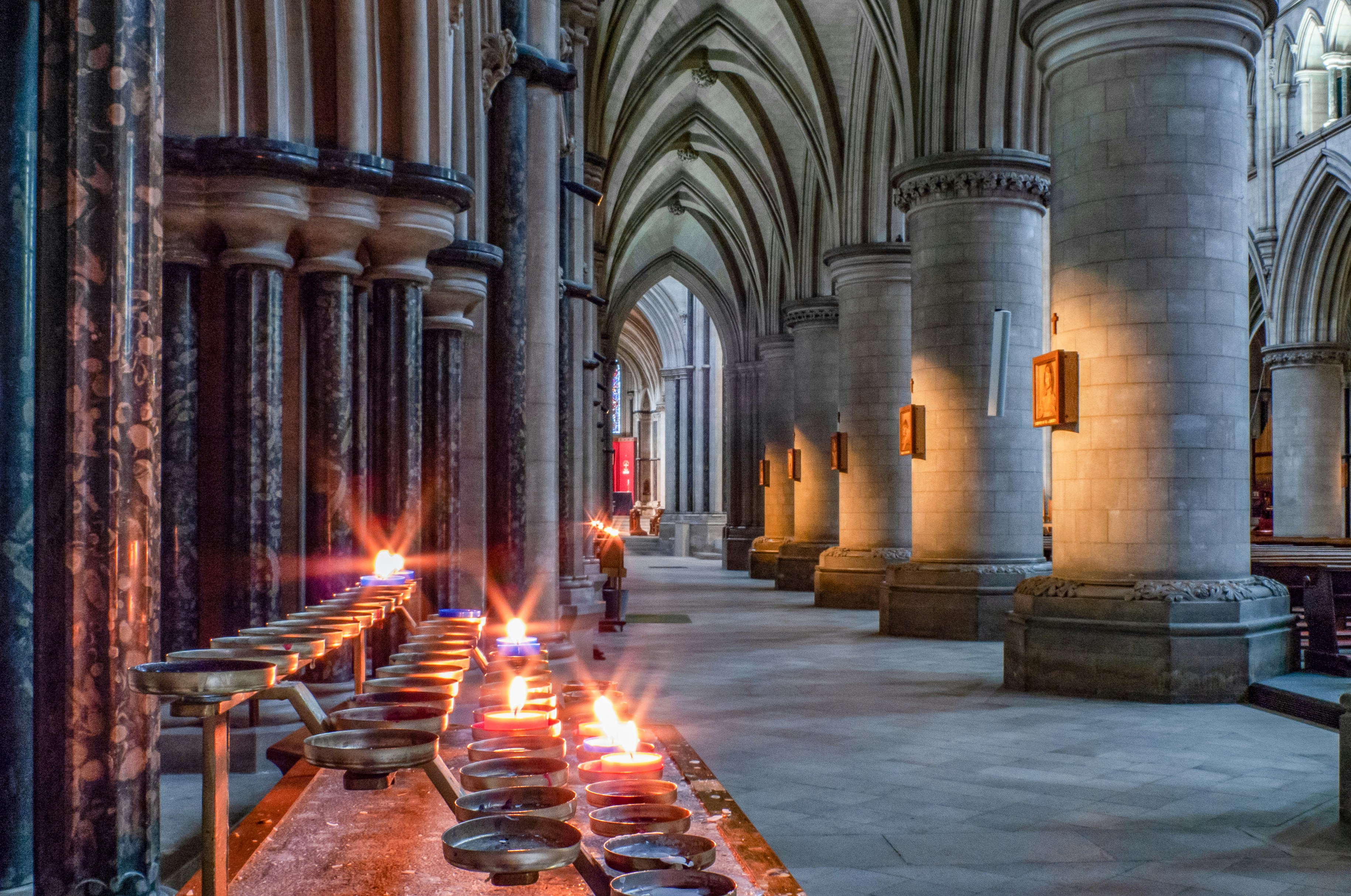 Lit candles line a long aisle in an old church.
