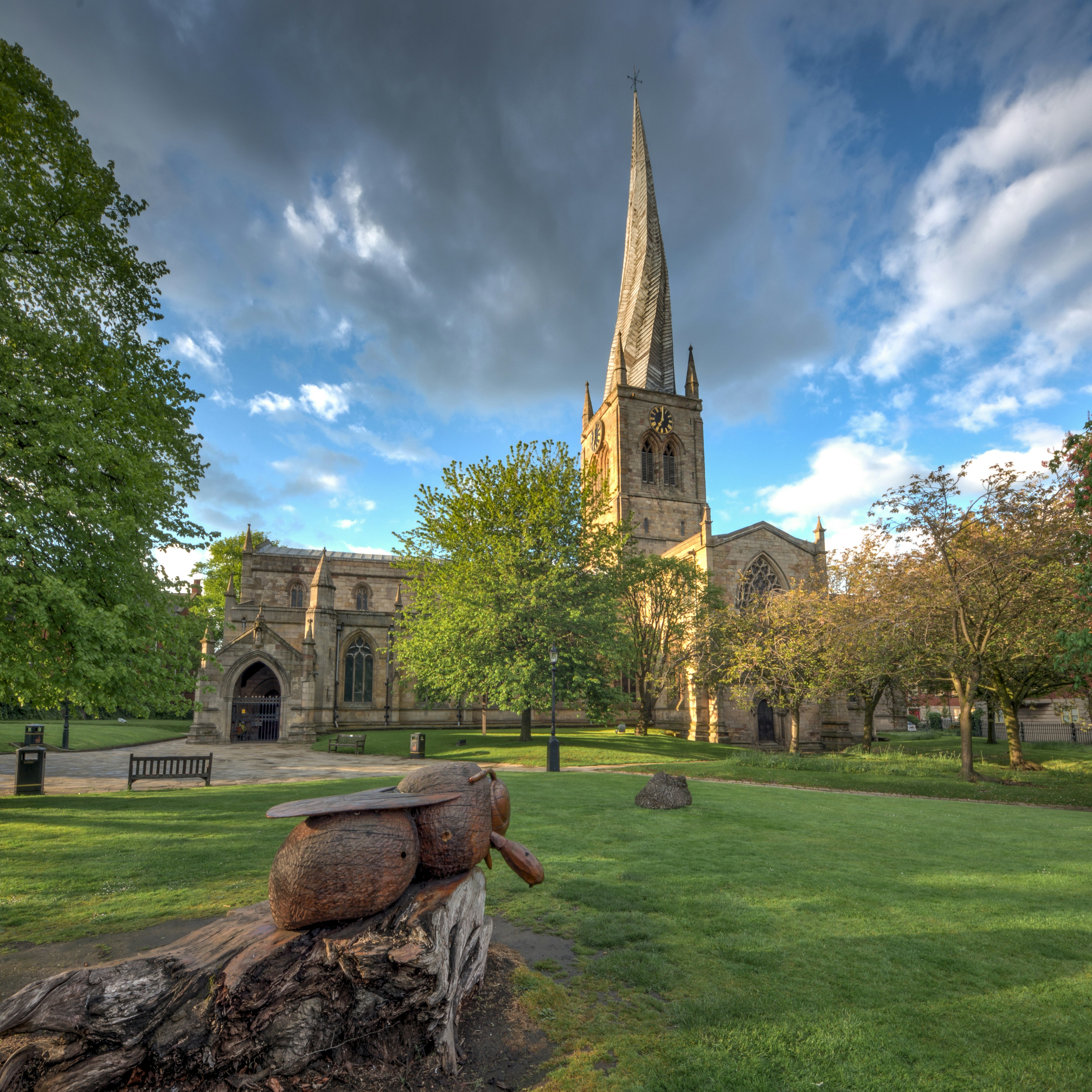 Stone spire against a sunlit park: cathedral foreground with a mossy sculpture