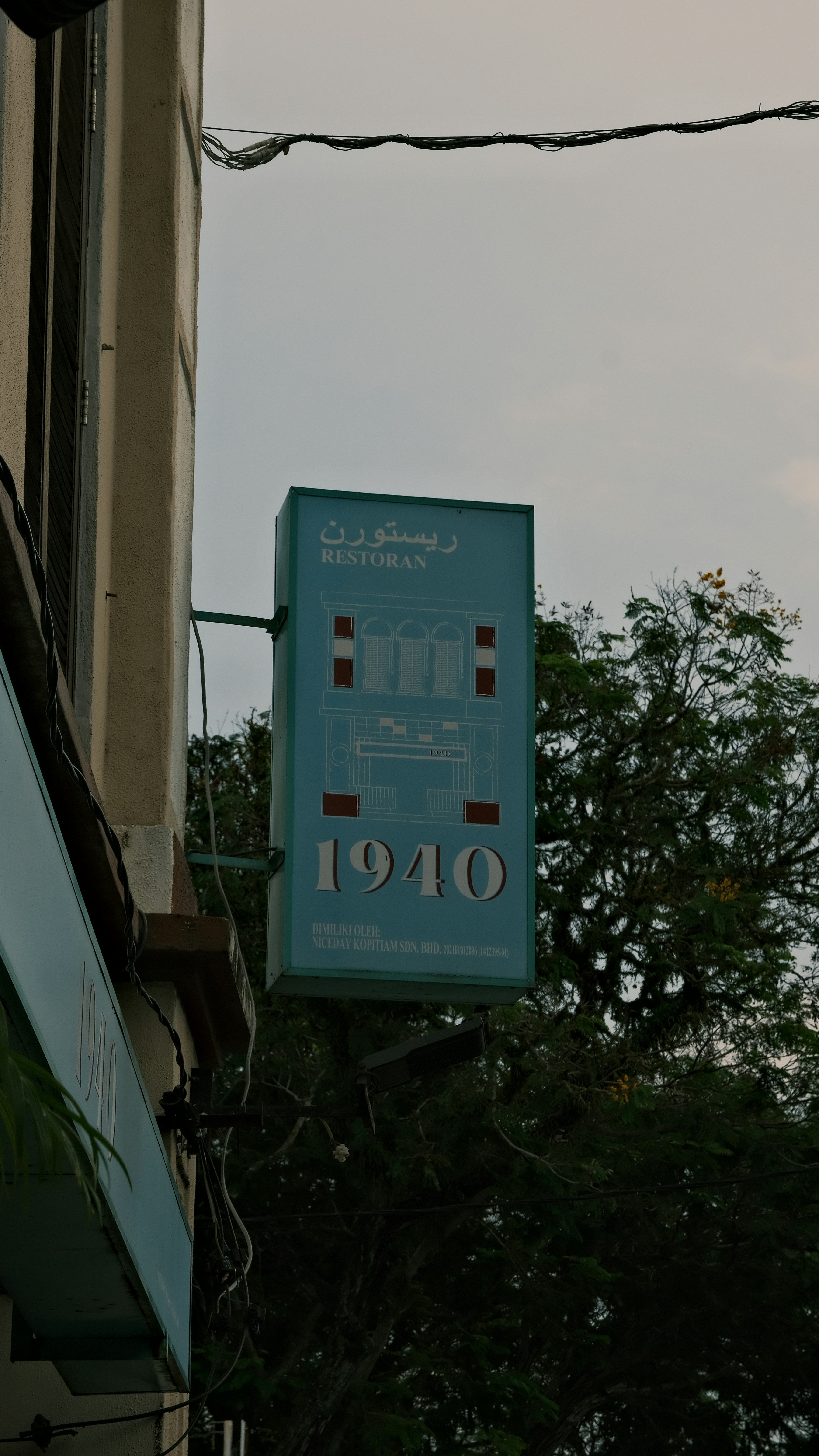 Blue Signage Above Street Level: 1940 Restoran Sign with Arabic Script