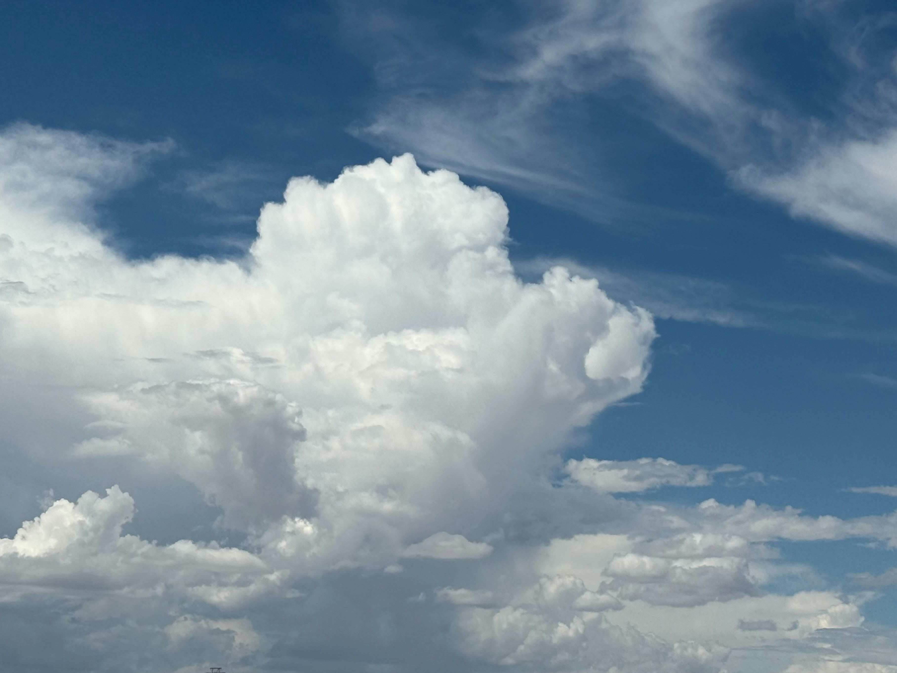 Bright cumulus clouds rise against a deep blue sky, occupying the upper two-thirds of the frame with soft edges and strong contrast to the horizon.