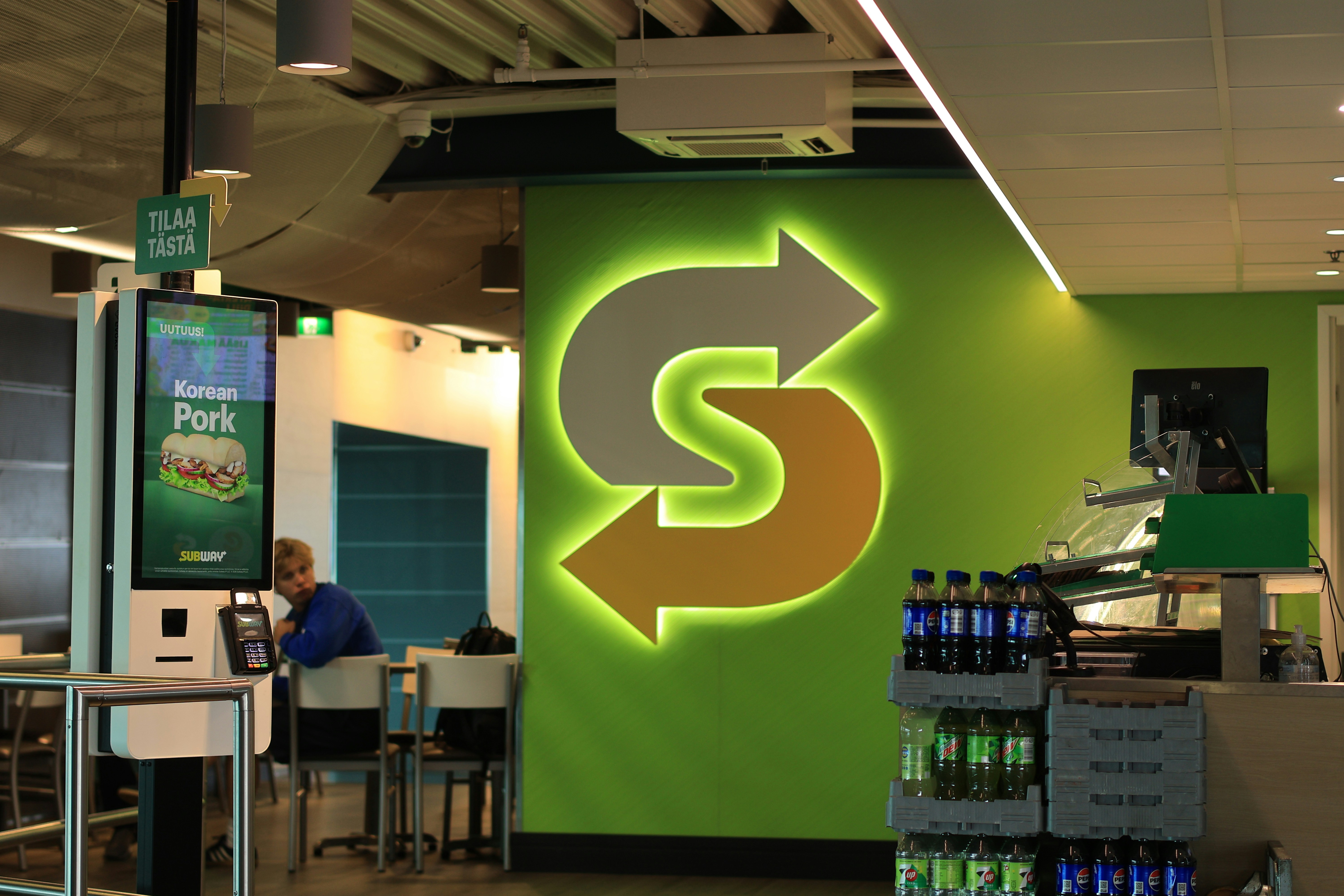 Neon Green Swirl Logo Overlaps a Busy Self-Checkout Area