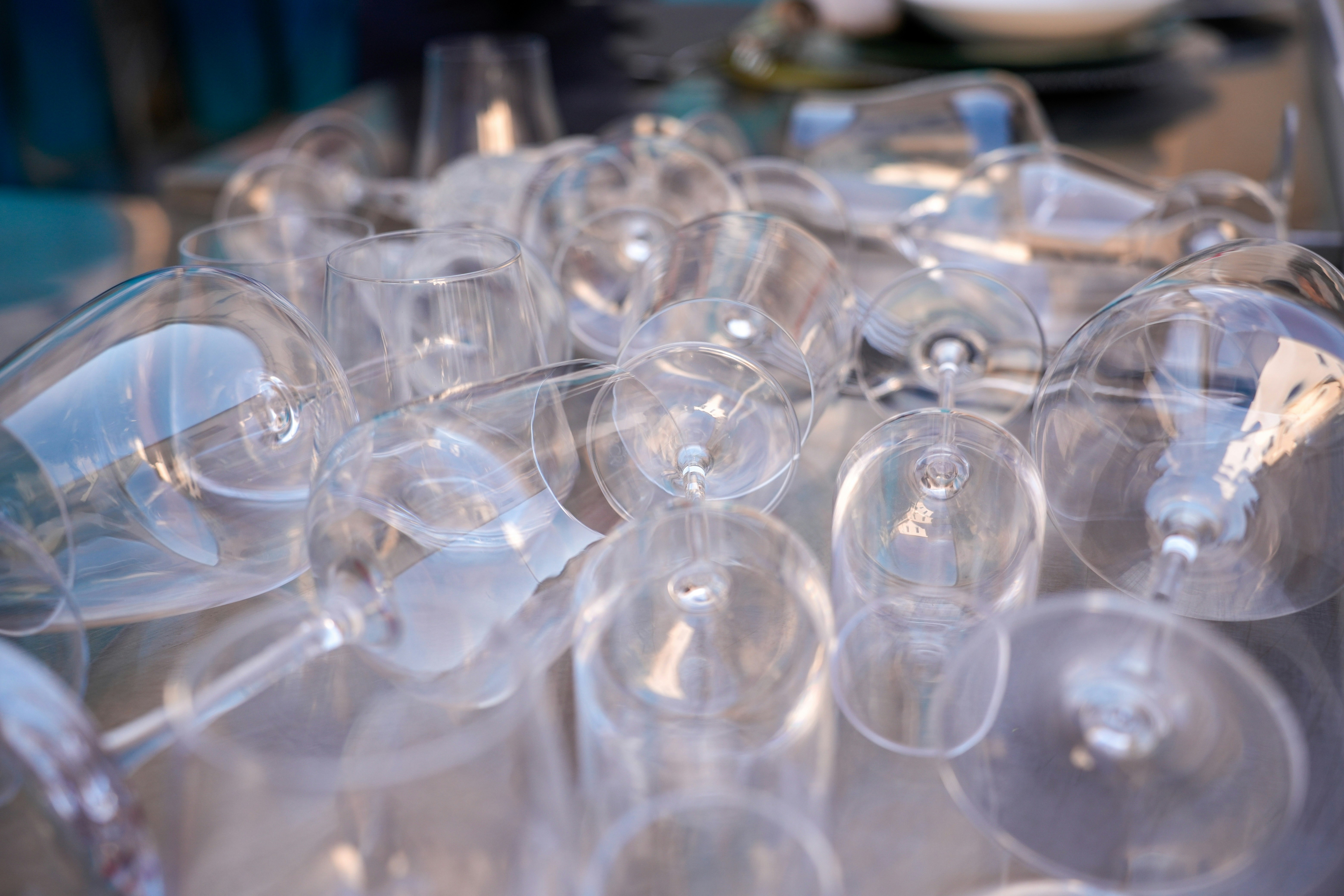 Close-up of overlapping wine glasses catching soft ambient light, creating a translucent mosaic of reflections and curves. Glassware arrangement suggests a dining setup, with a calm, blurred background.