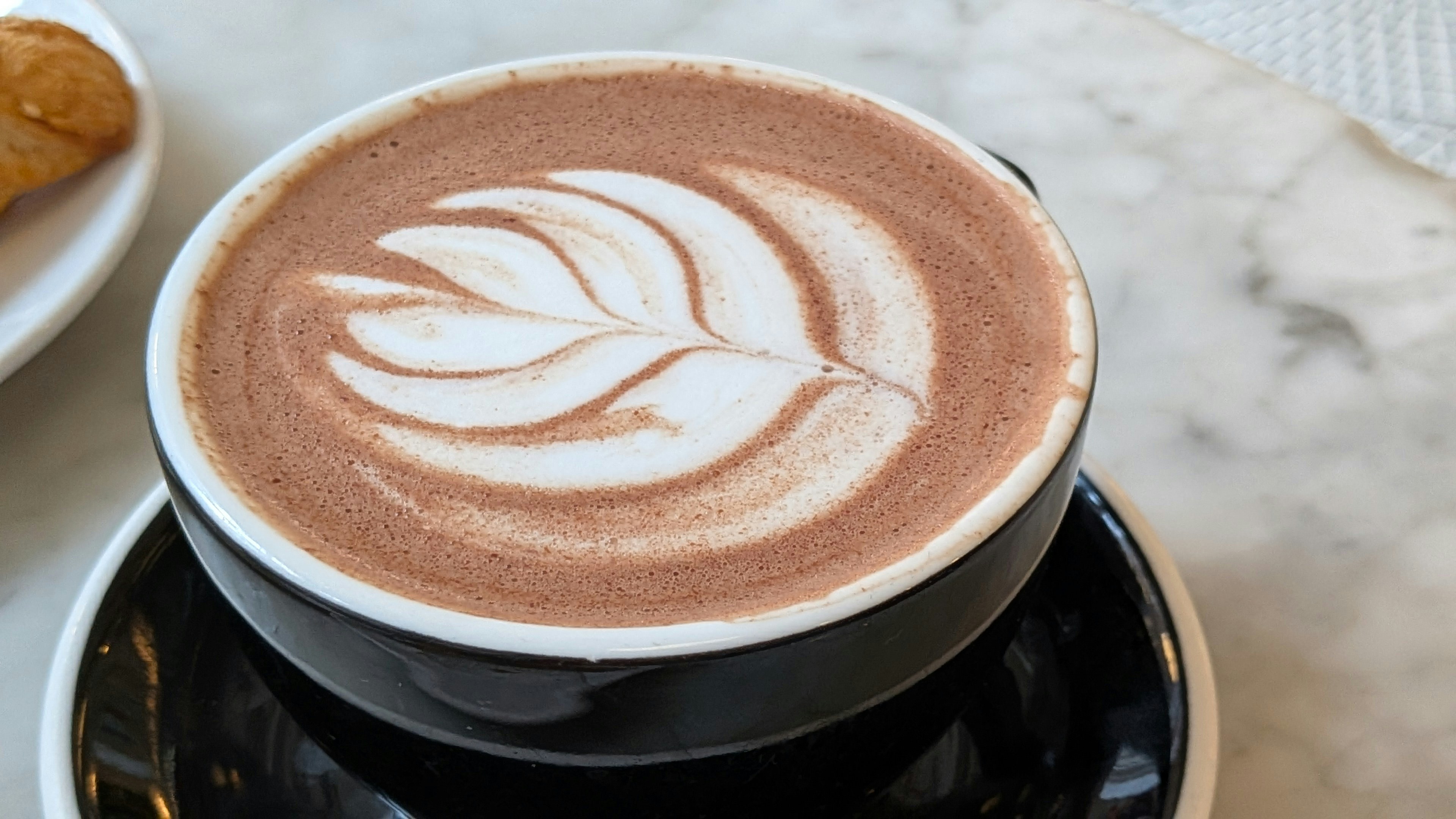 Creamy latte with a rosetta pattern sits on a dark cup atop a marble table.