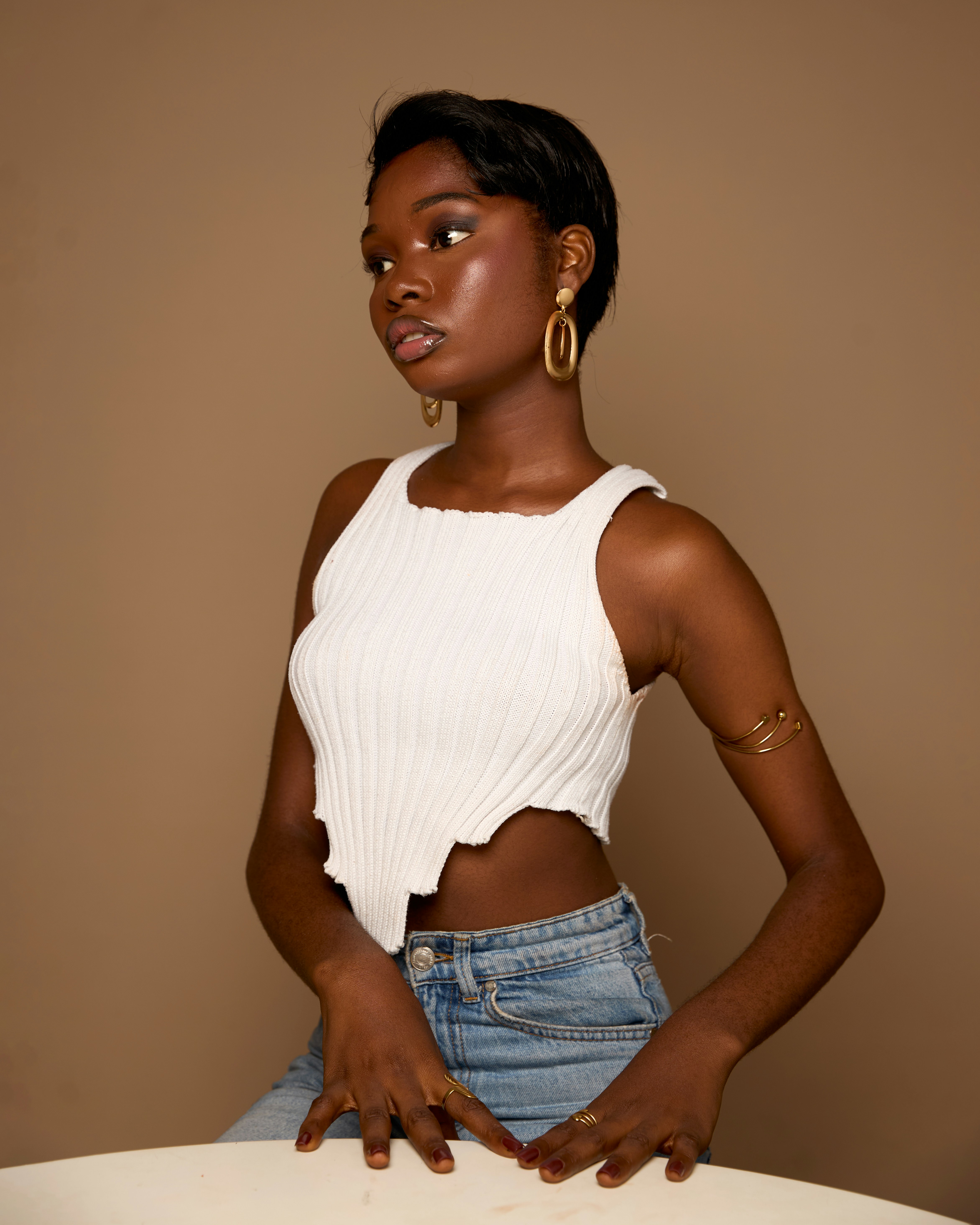  confident silhouette: gold hoops and white knit under warm tan backdrop