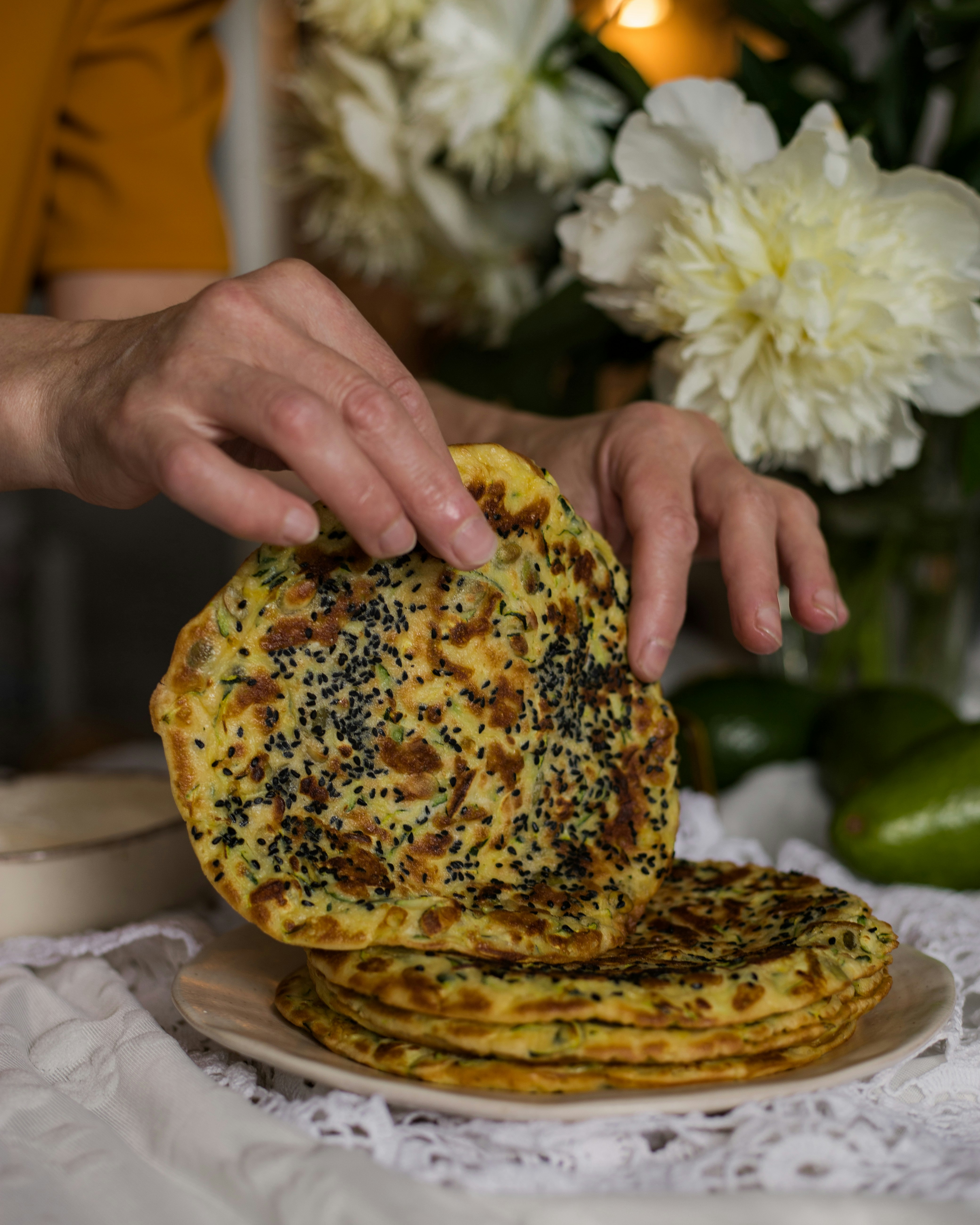 Hands Stack Golden Flatbreads Beneath a Flourishing Floral Backdrop