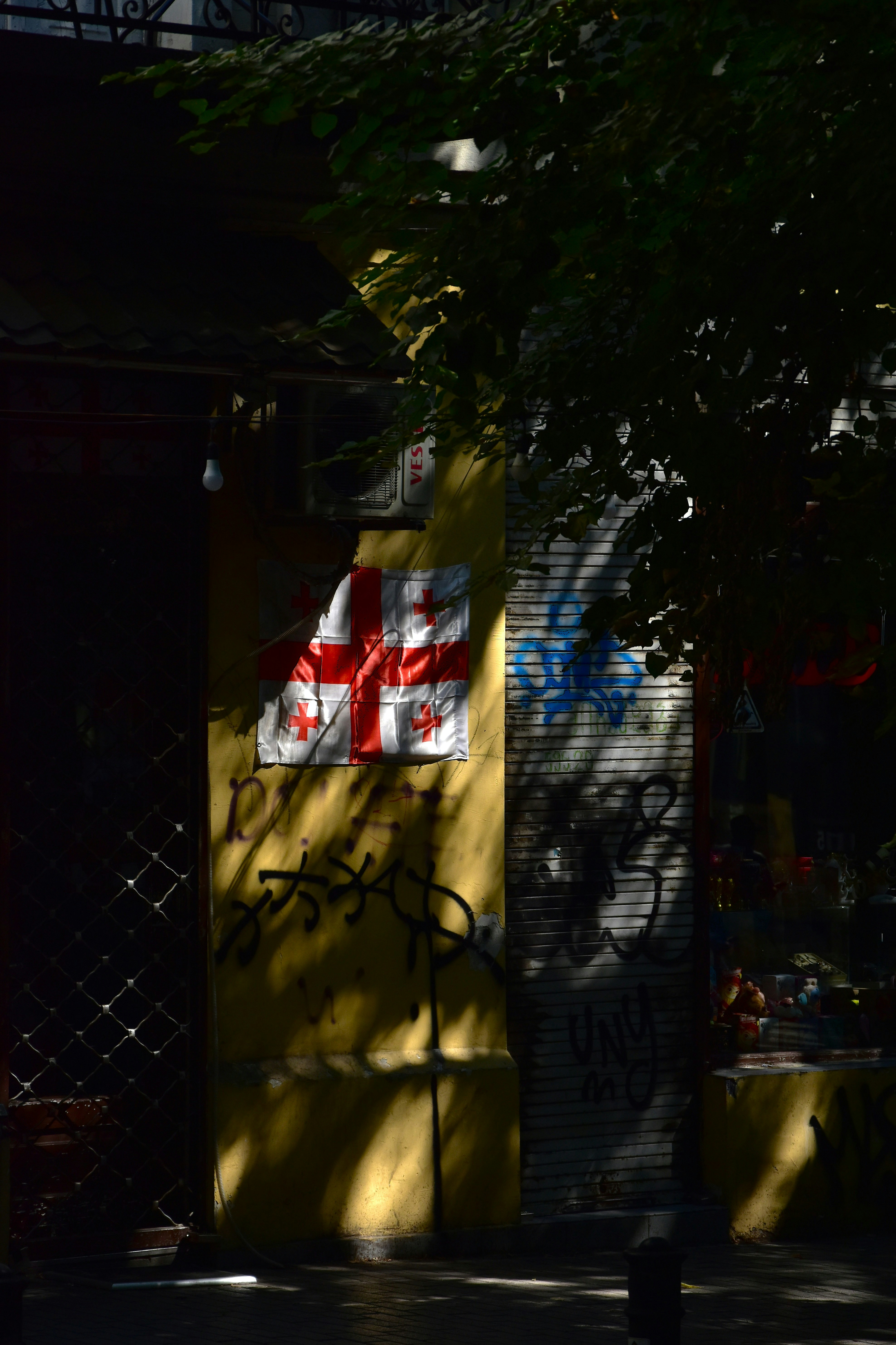 Georgia’s Passage: A Dark Allée Framed by Graffiti and Sunlit Georgia Cross