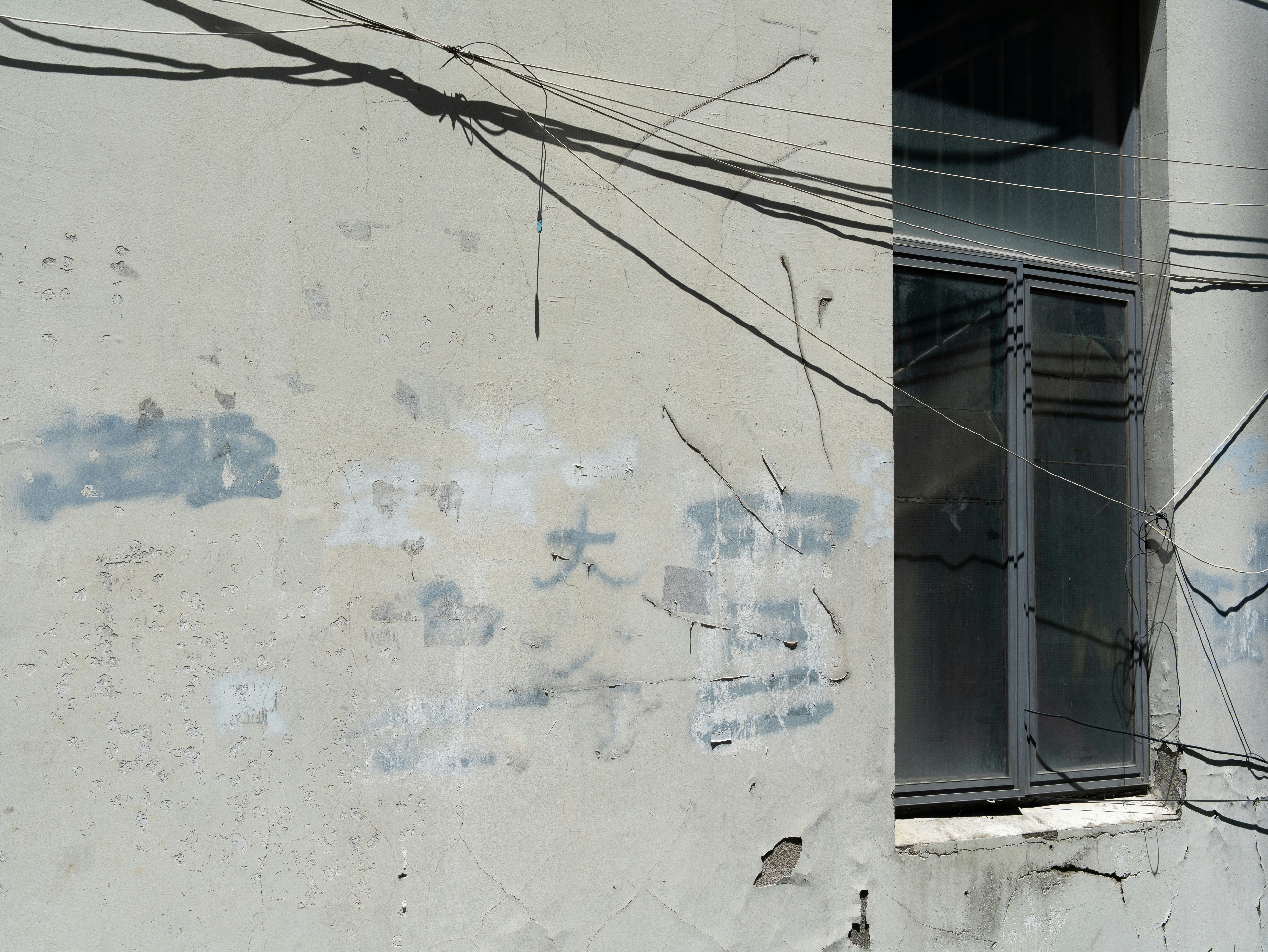 Weathered Wall Secrets: Faded Letters and Wires in Quiet Noon