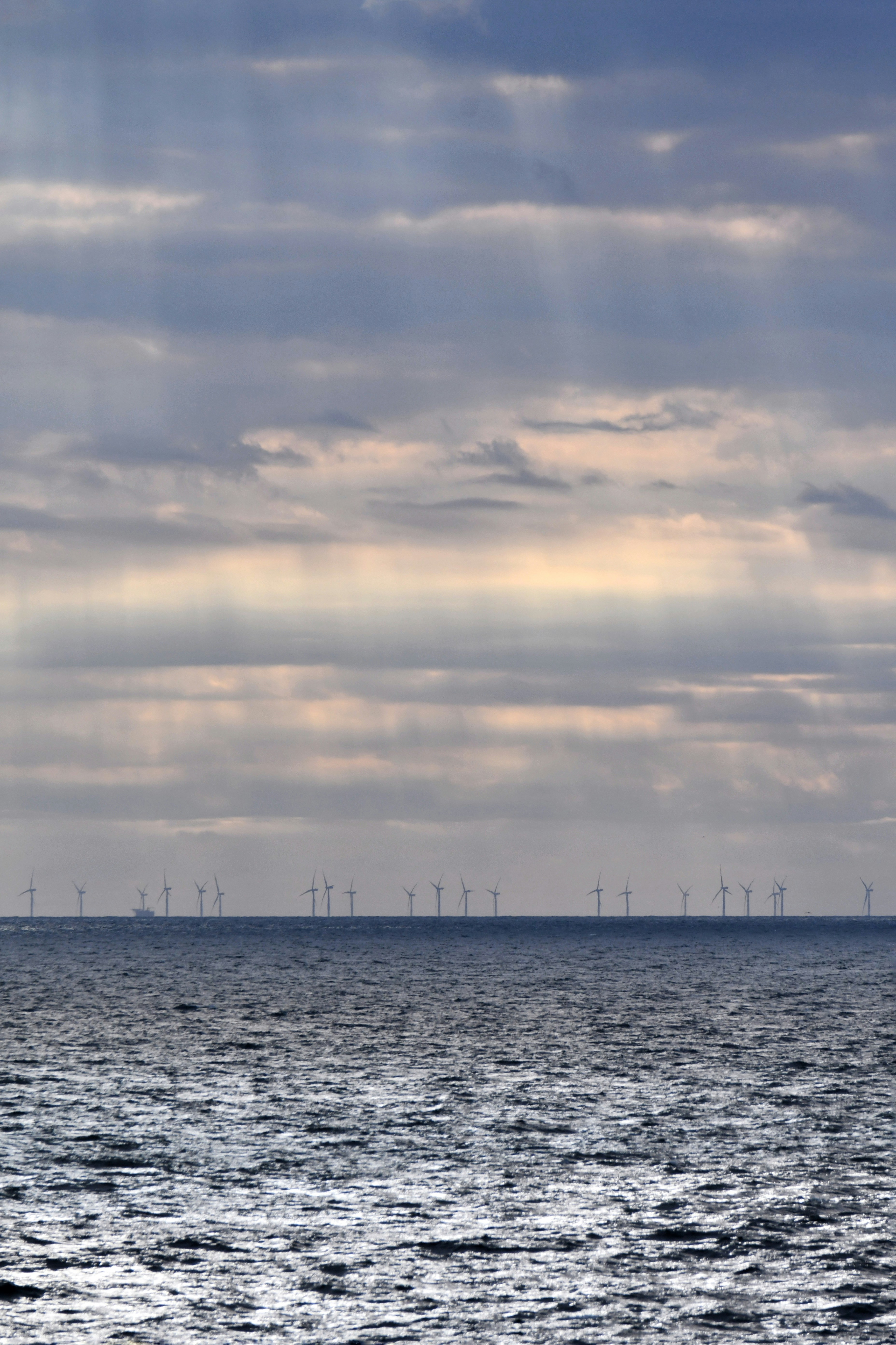 Line of distant wind turbines at sea under a moody layered sky