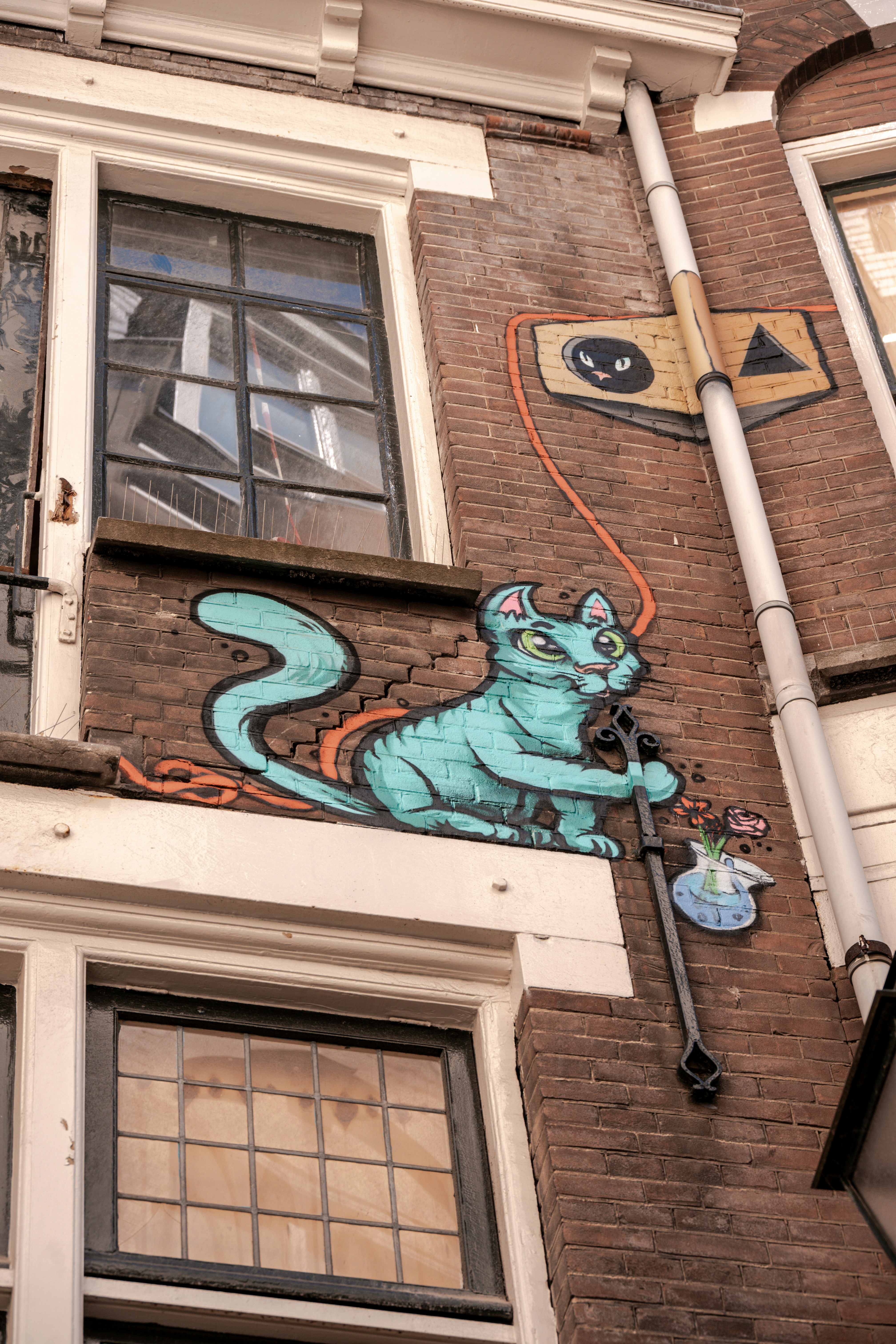Turquoise alley-cat mural anchors a brick façade with a playful twist