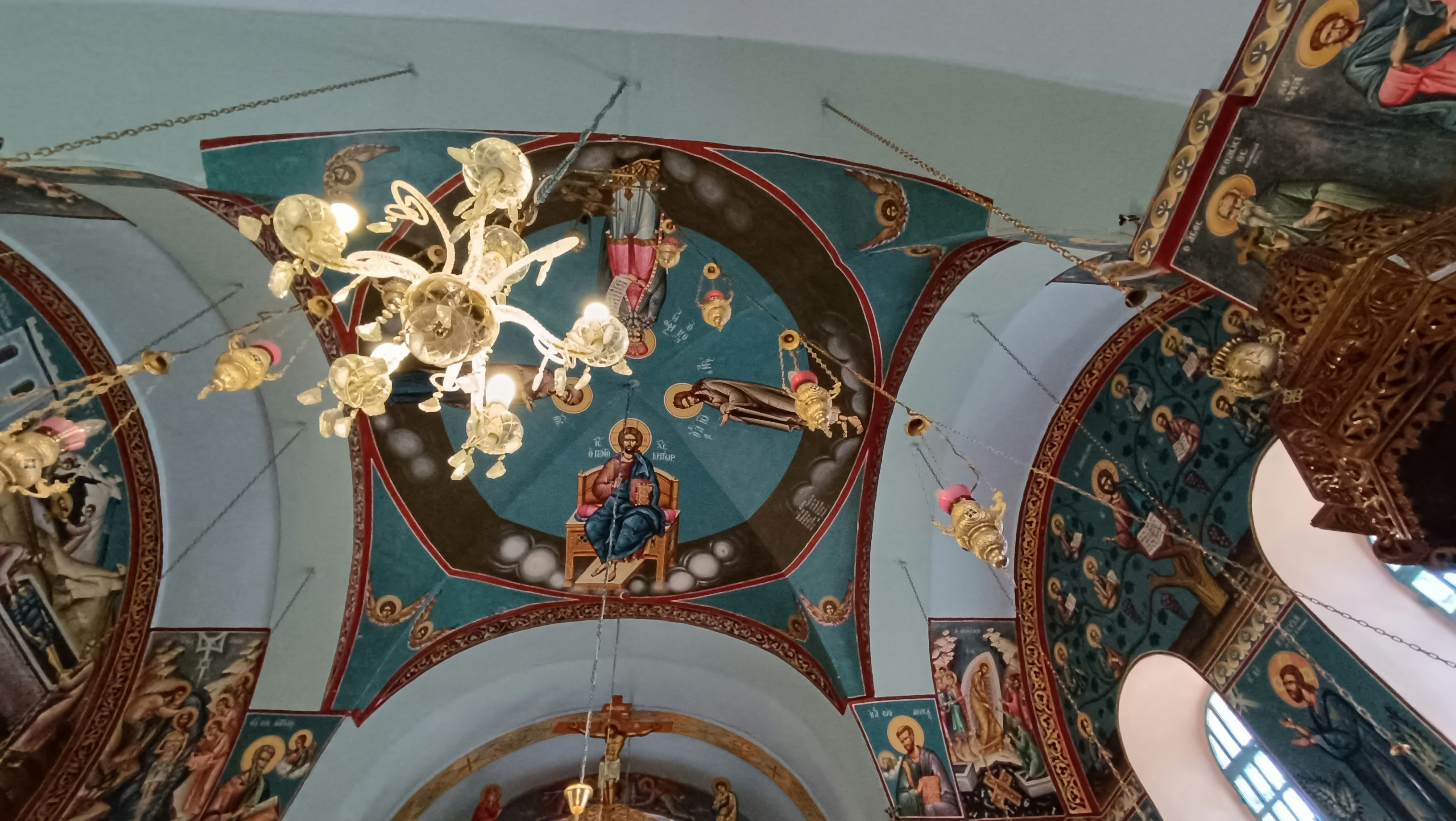 Ornate religious ceiling with frescoes and a chandelier, captured to emphasize architectural details and color-rich artwork in a dim interior.
