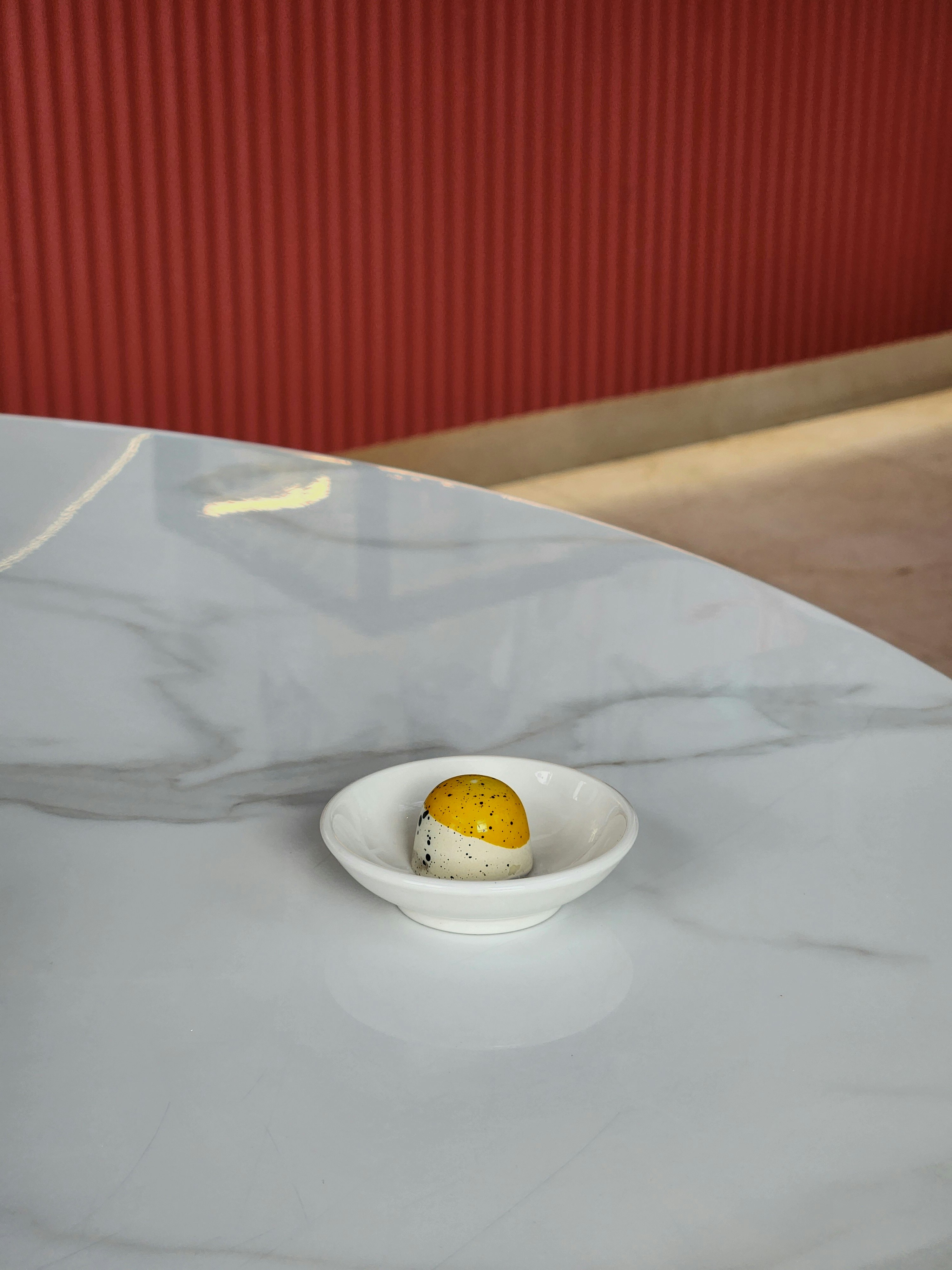 Minimal still life: the speckled egg in a white dish on a marble table