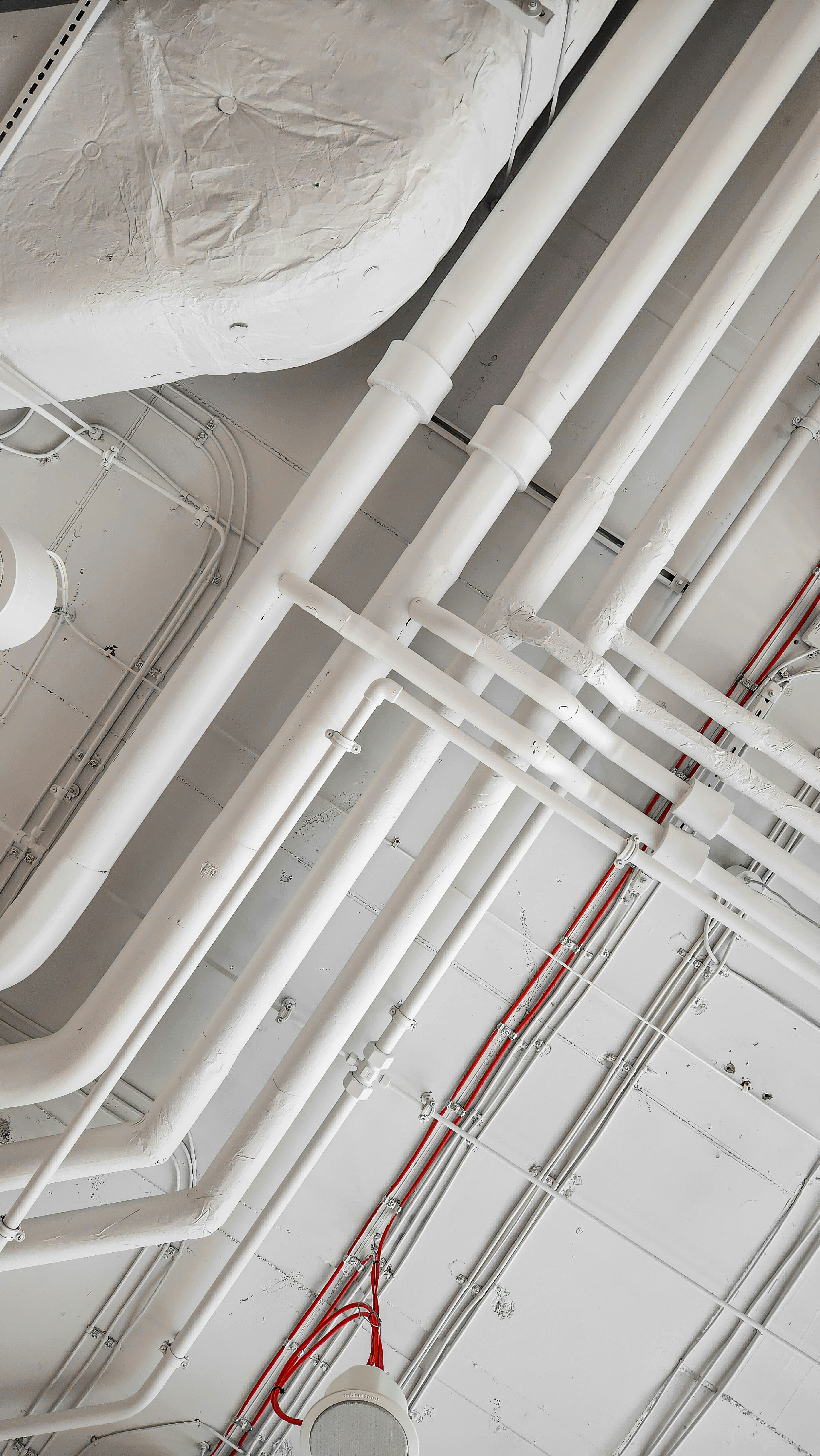 Industrial Maze: White Pipes and Red Cables Under Quiet Concrete Ceilings