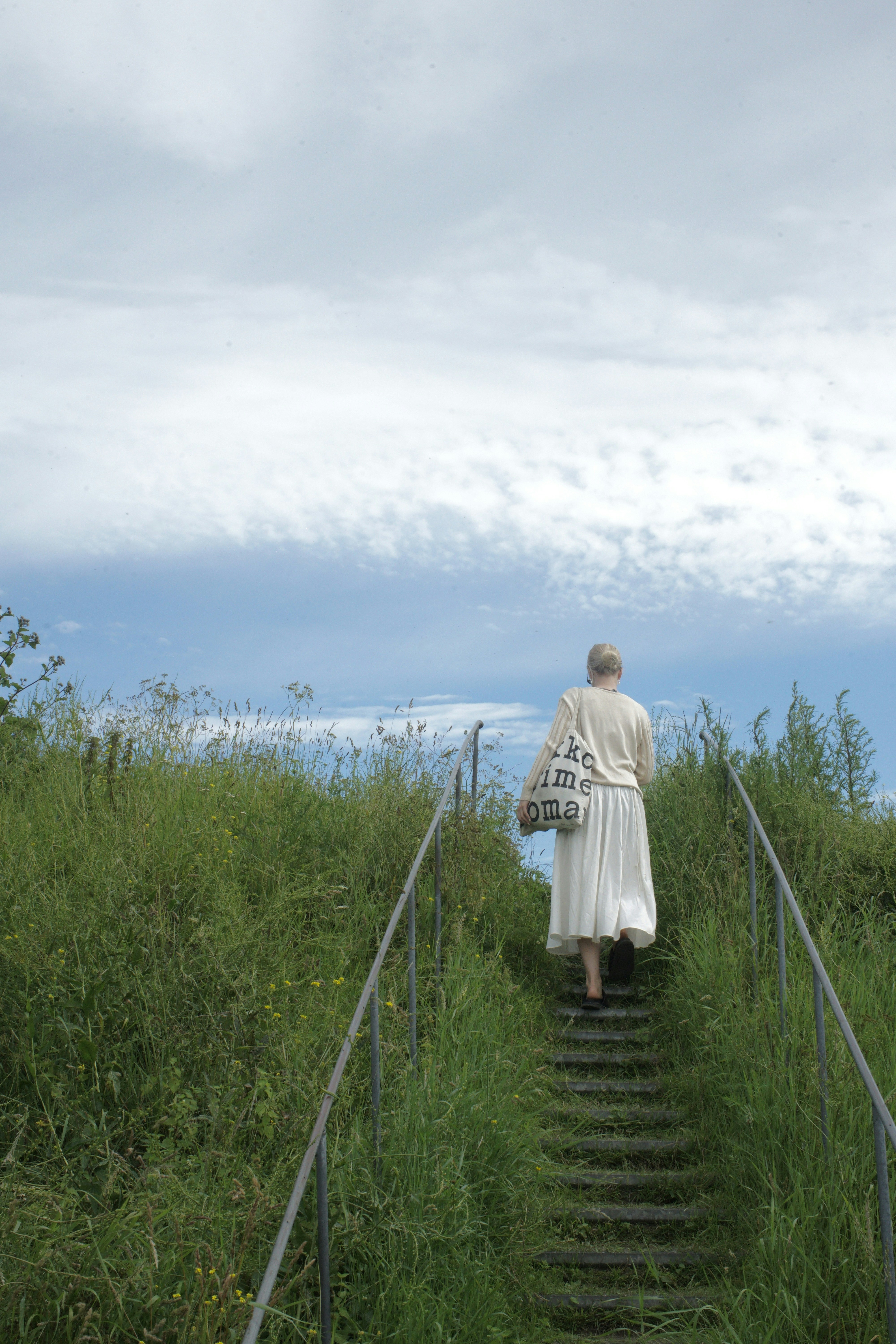 Woman Ascends a Green Stairway into a Cloudy Sky
