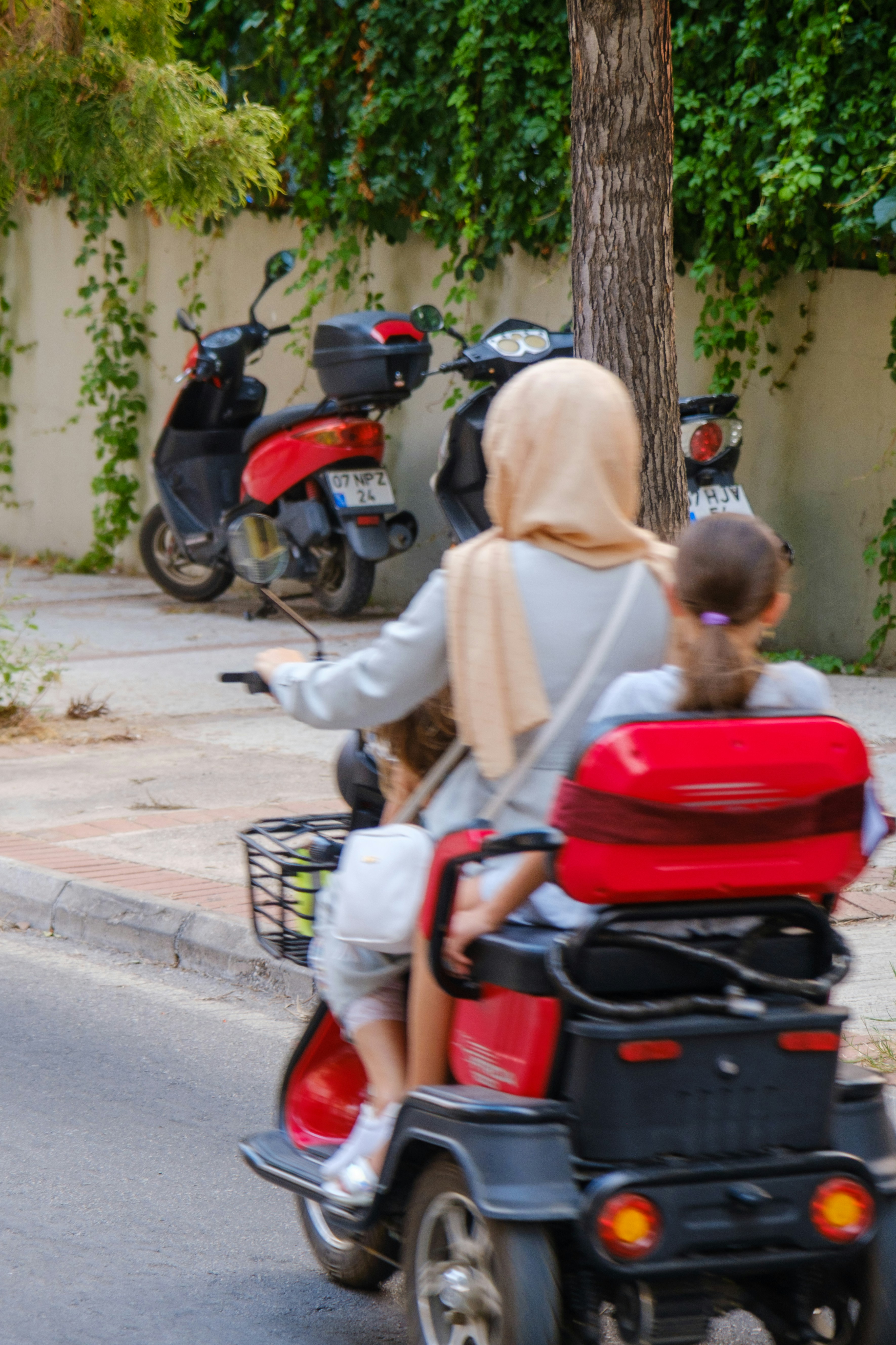 Two Riders on a Red Scooter Travel Past a Quiet Street Scene