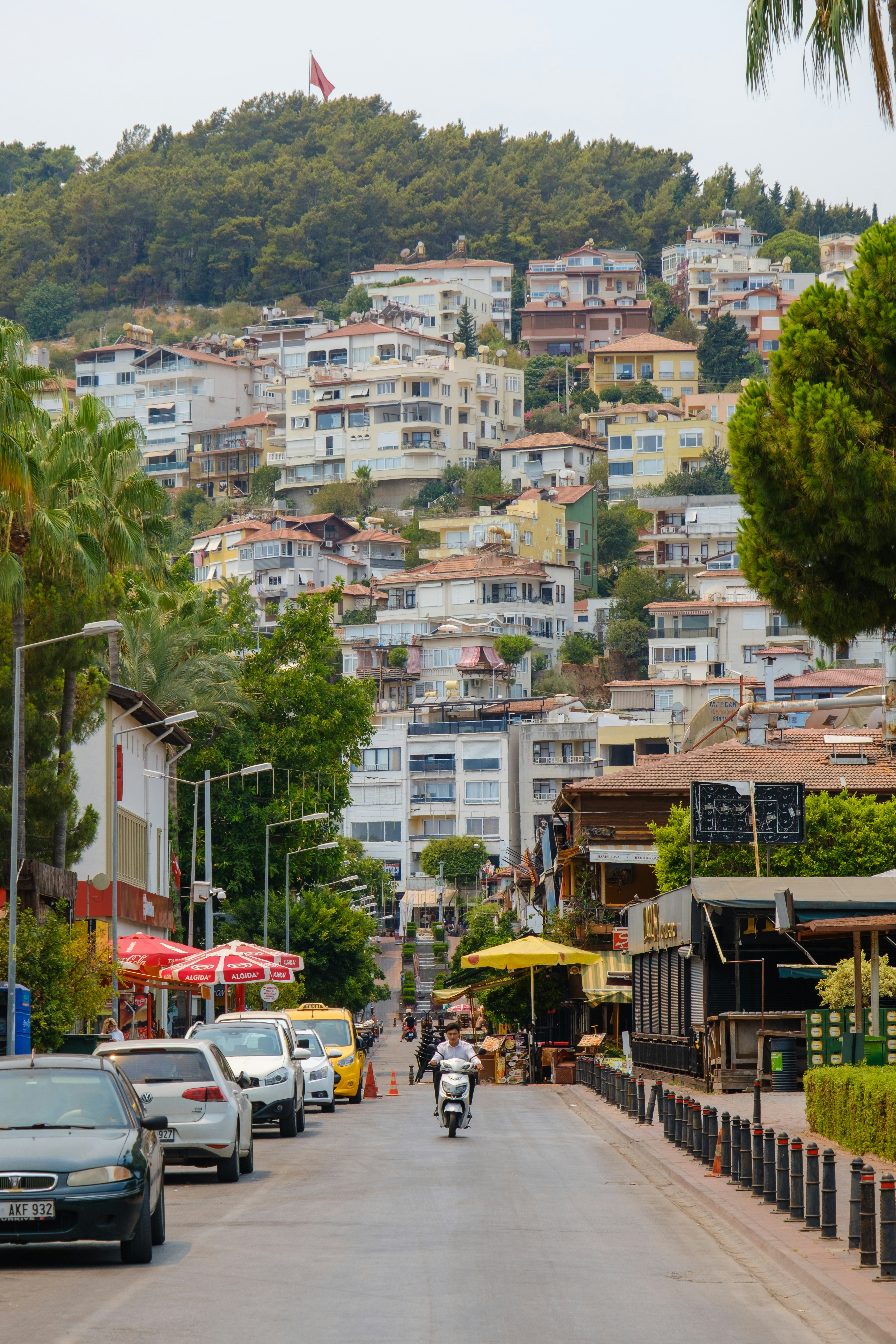 Terraced hillside streetscape: cars, scooter, and sunlit apartments