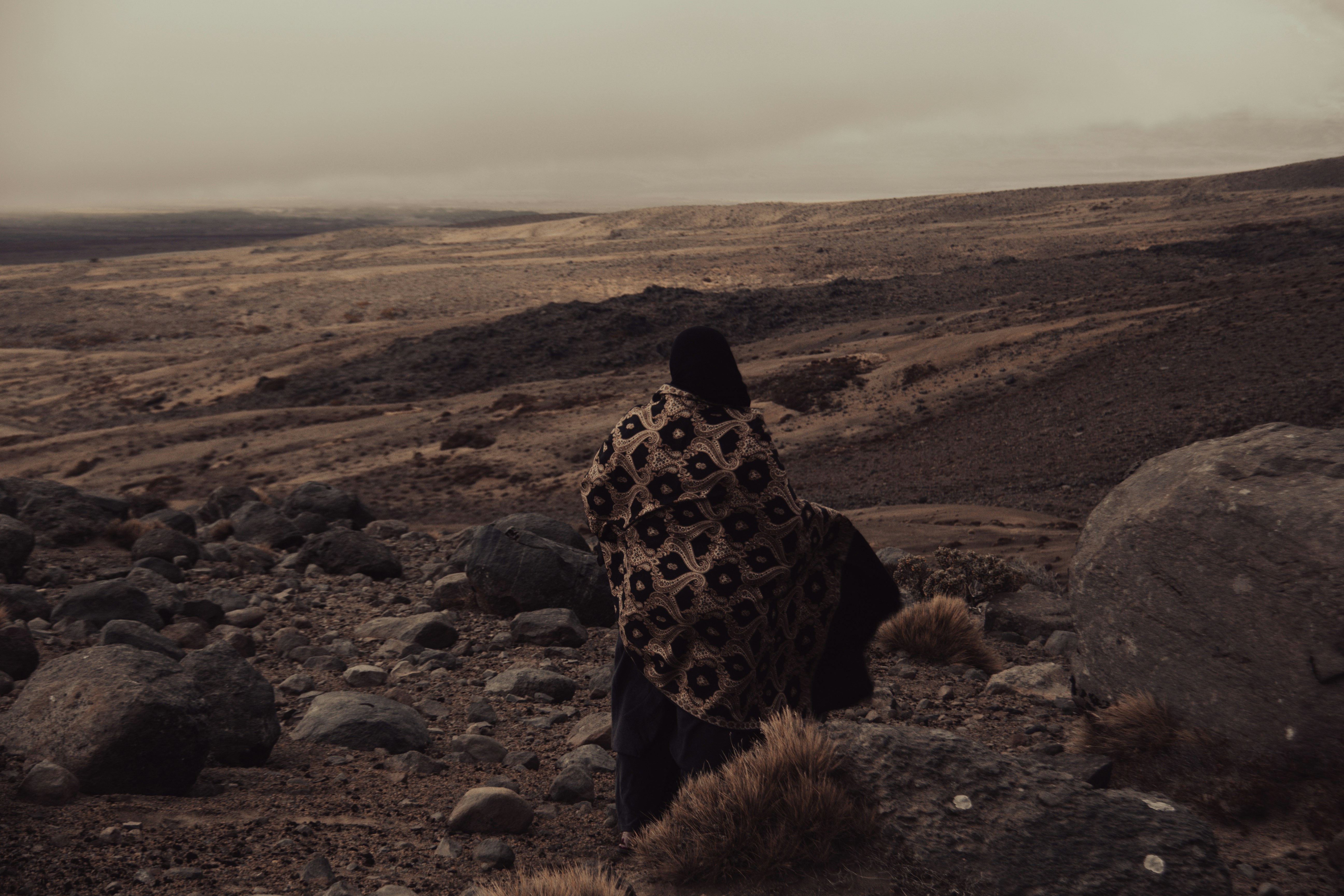 Traveler in a Desert Outcrop Wrapped in Patterned Cloak