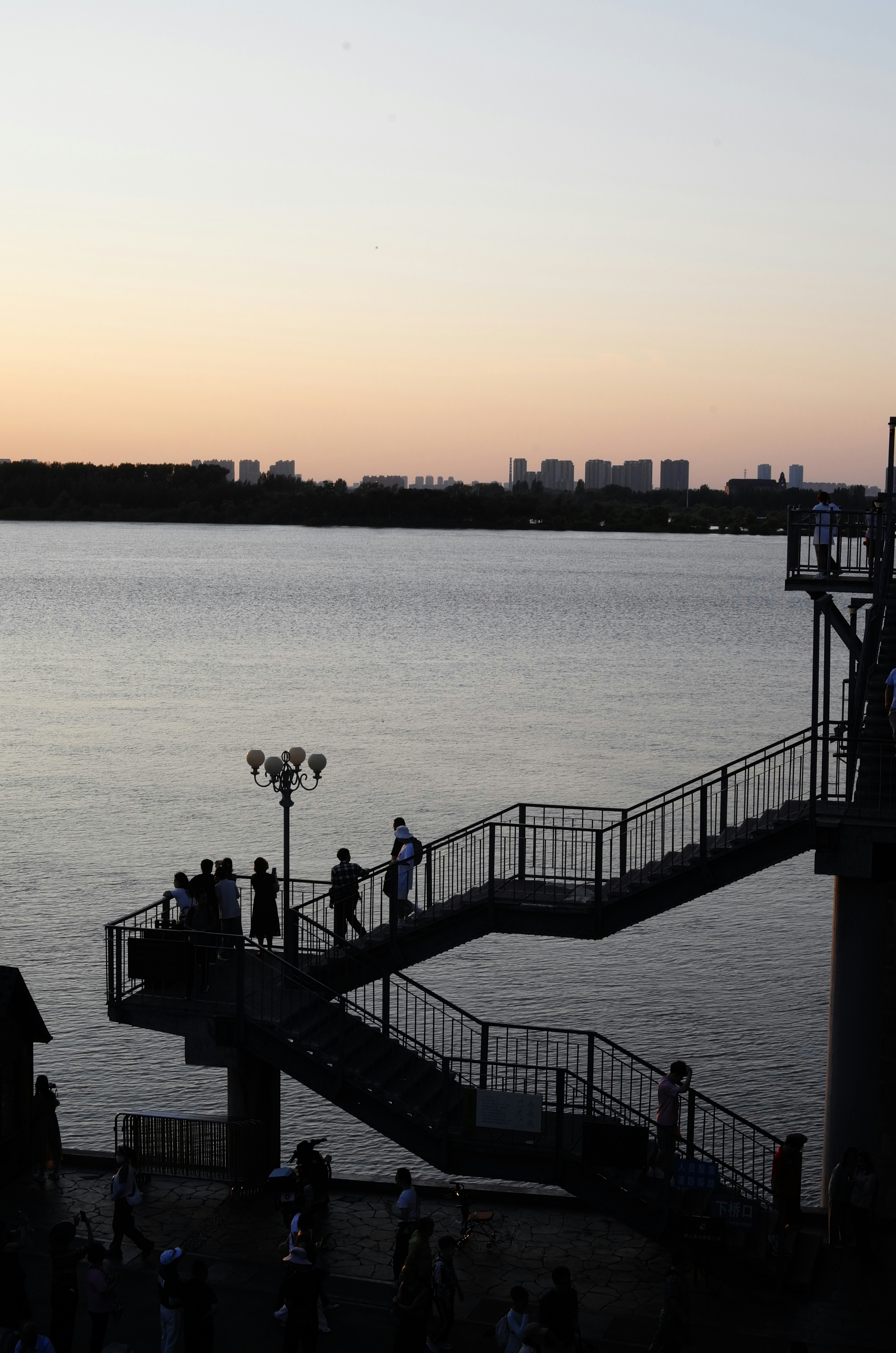Silhouetted walkway over calm waterfront at dusk