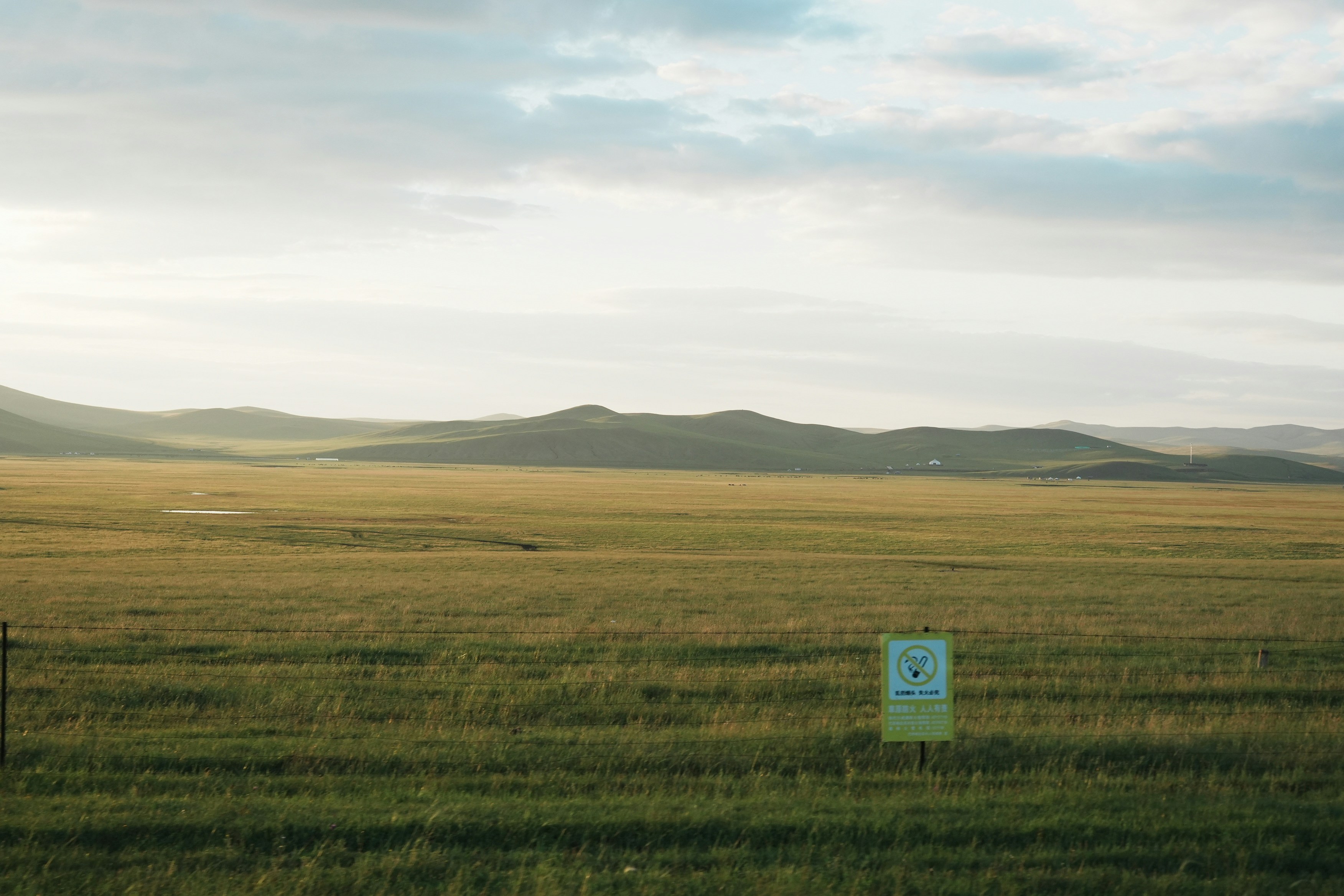 Wide open grassland with distant low hills and a single sign standing in the foreground; a calm, expansive landscape emphasizing openness. (photographic landscape).