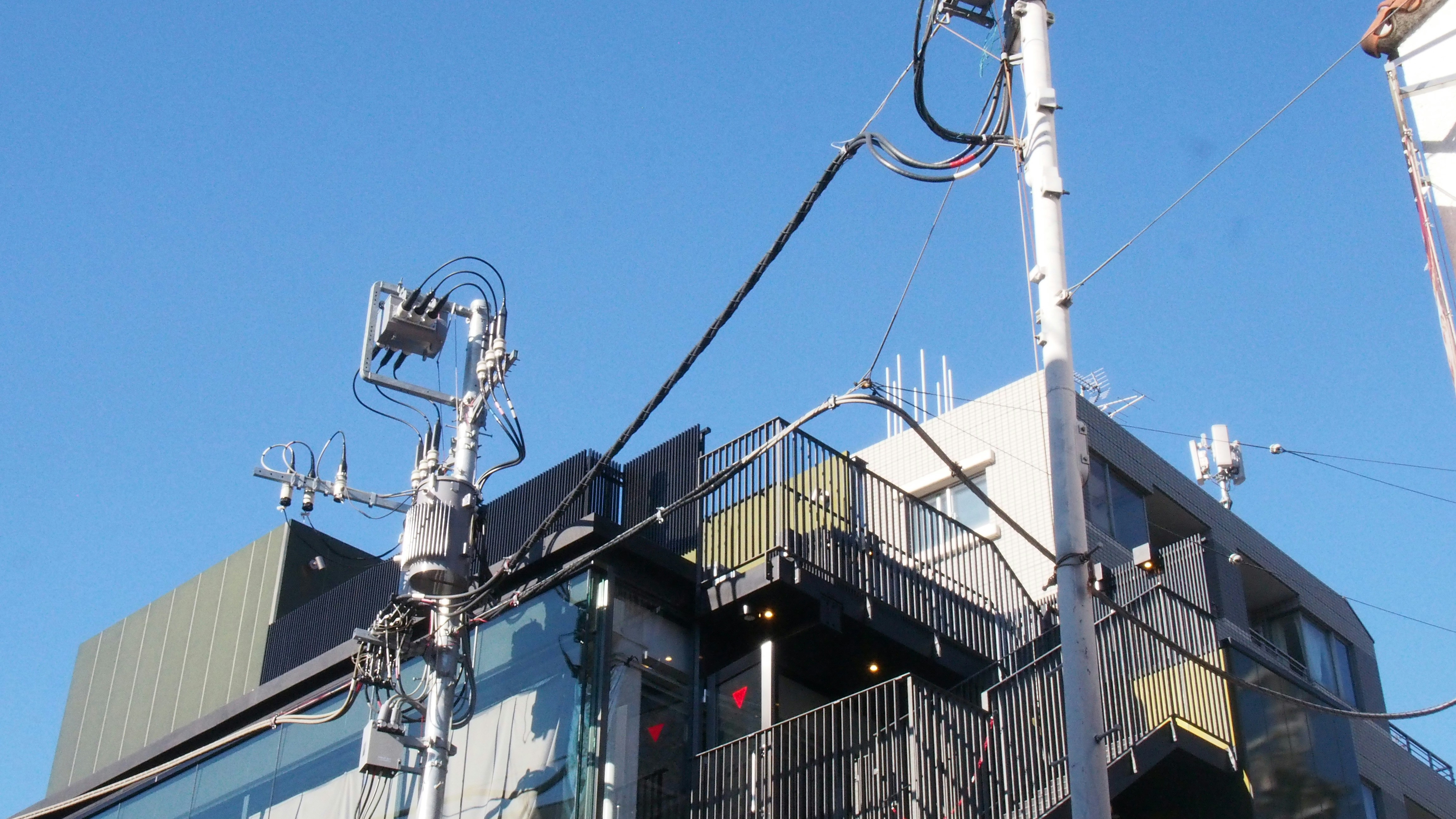 Rooftop structures, vents, and power lines against a bright blue sky atop a modern multi-level building.