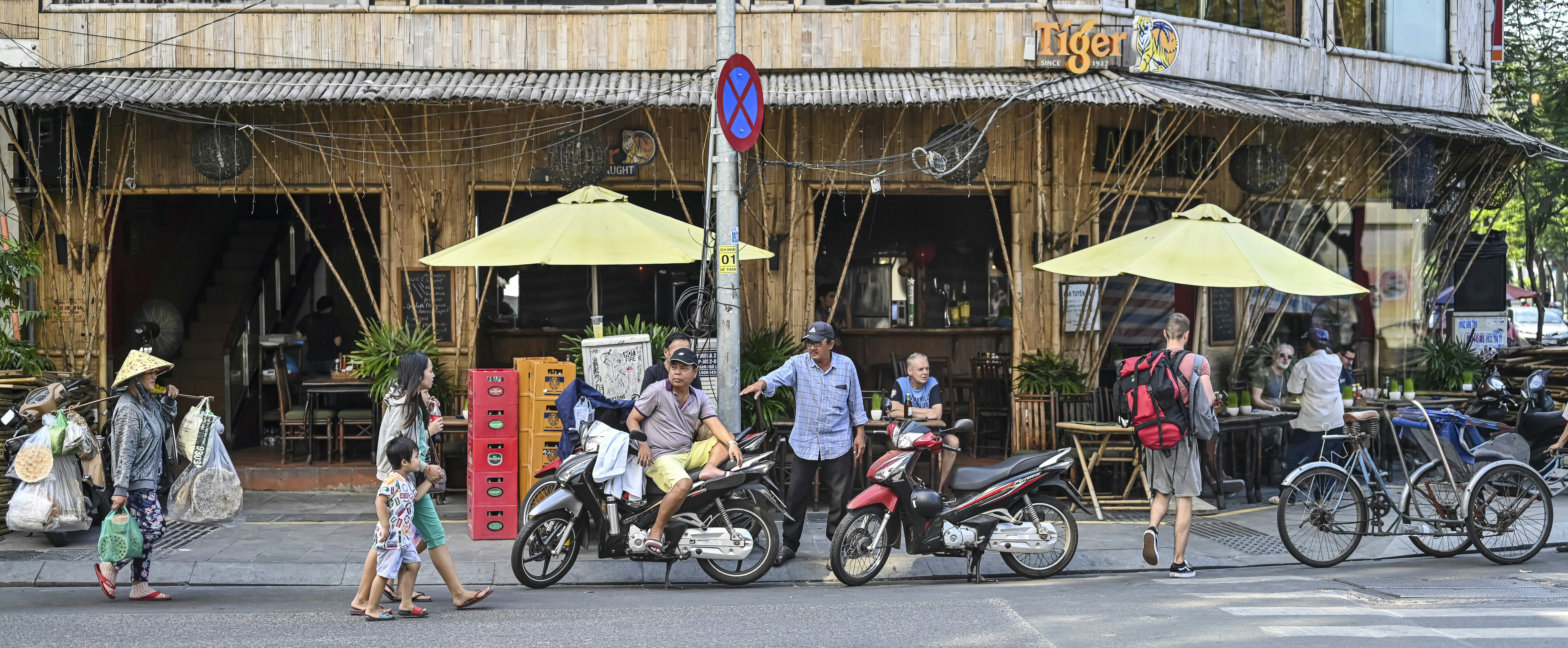 Street Café Nexus: Motorbikes, Umbrellas, and a Busy Crosswalk