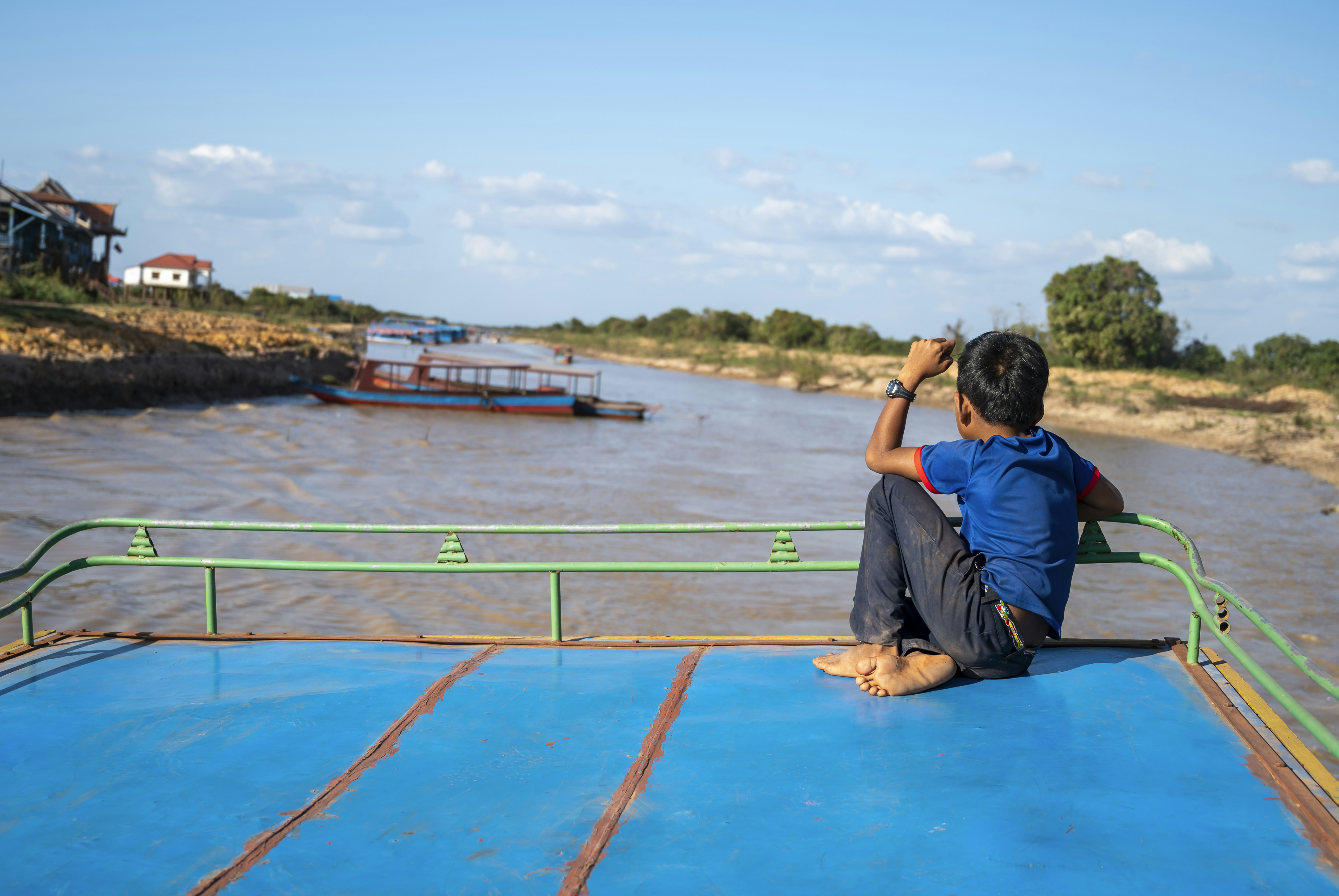 Child on a blue boat deck gazes toward distant riverbank and boats