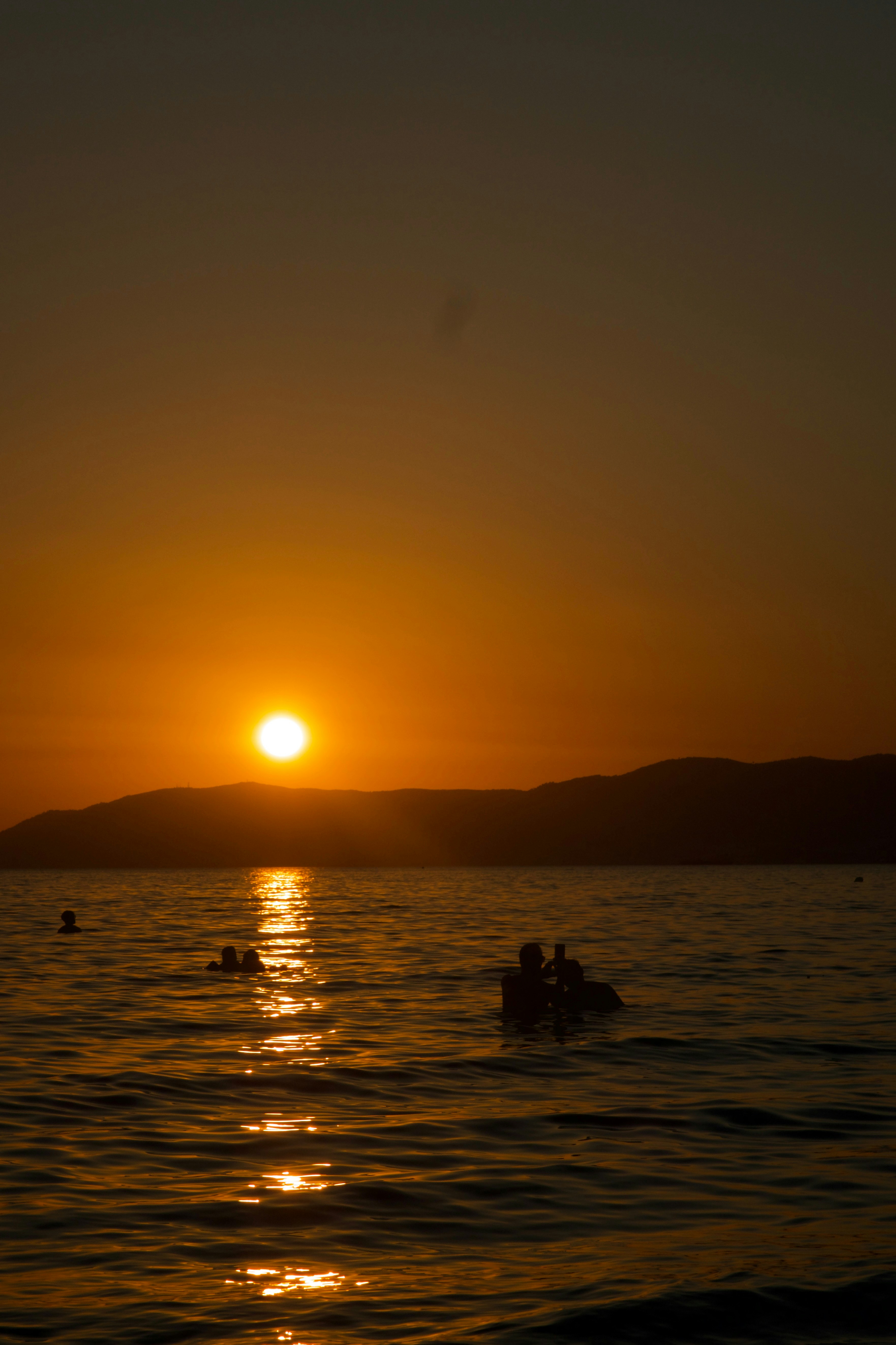 Sunset over tranquil sea with silhouettes at water’s edge