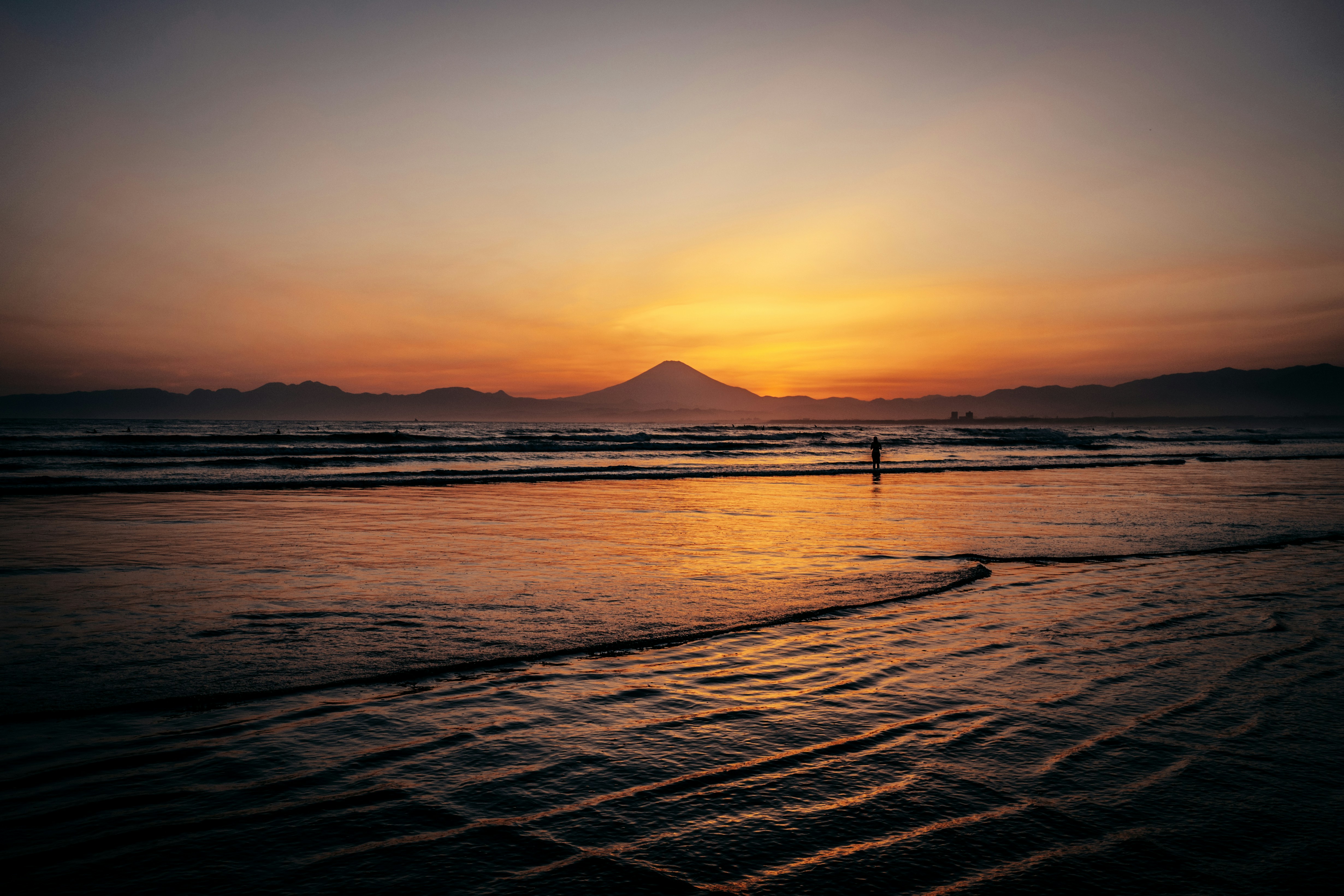 Sunset over a quiet shoreline with a distant volcanic silhouette