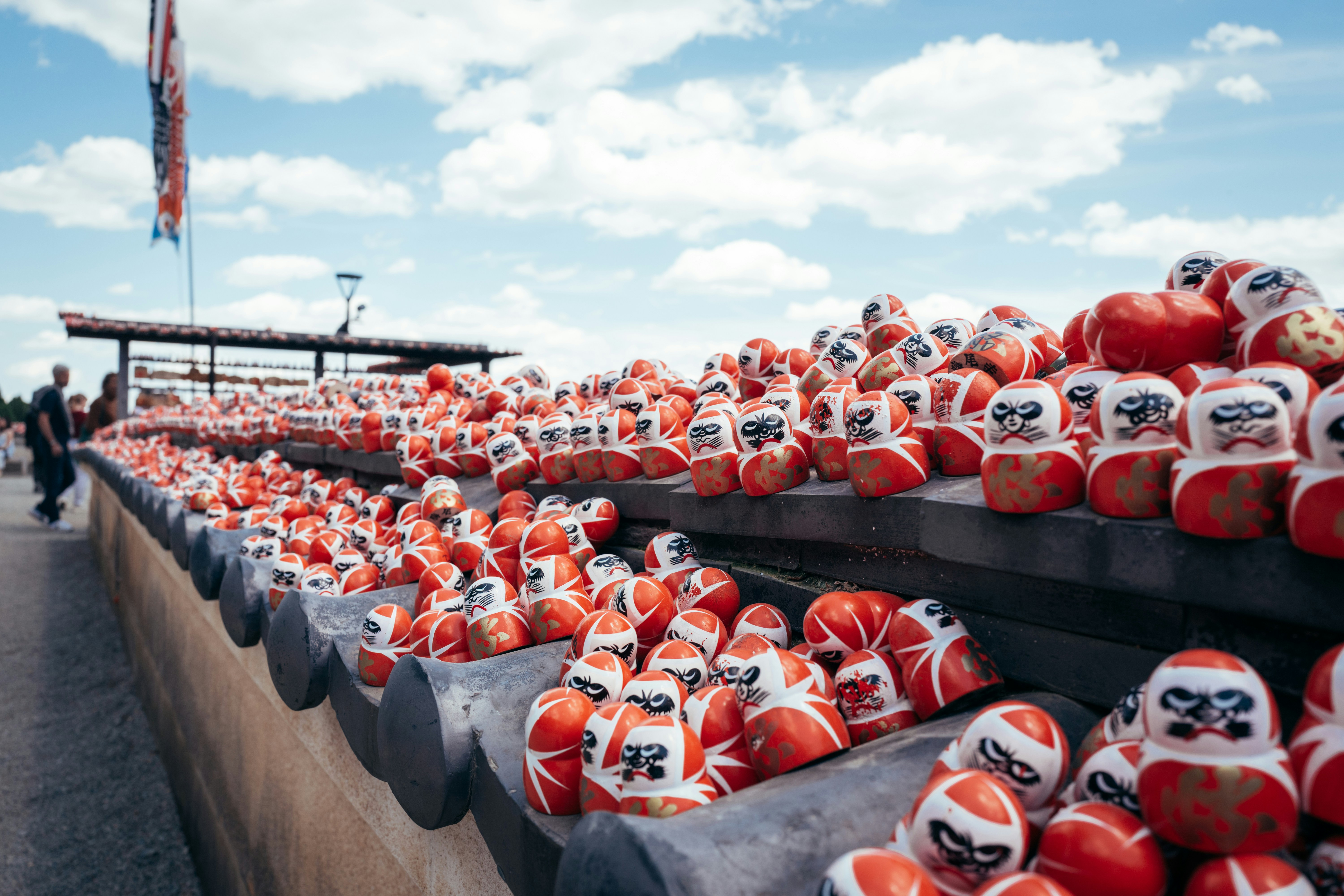 Row of Daruma on a Concrete Barrier by the Shoreline