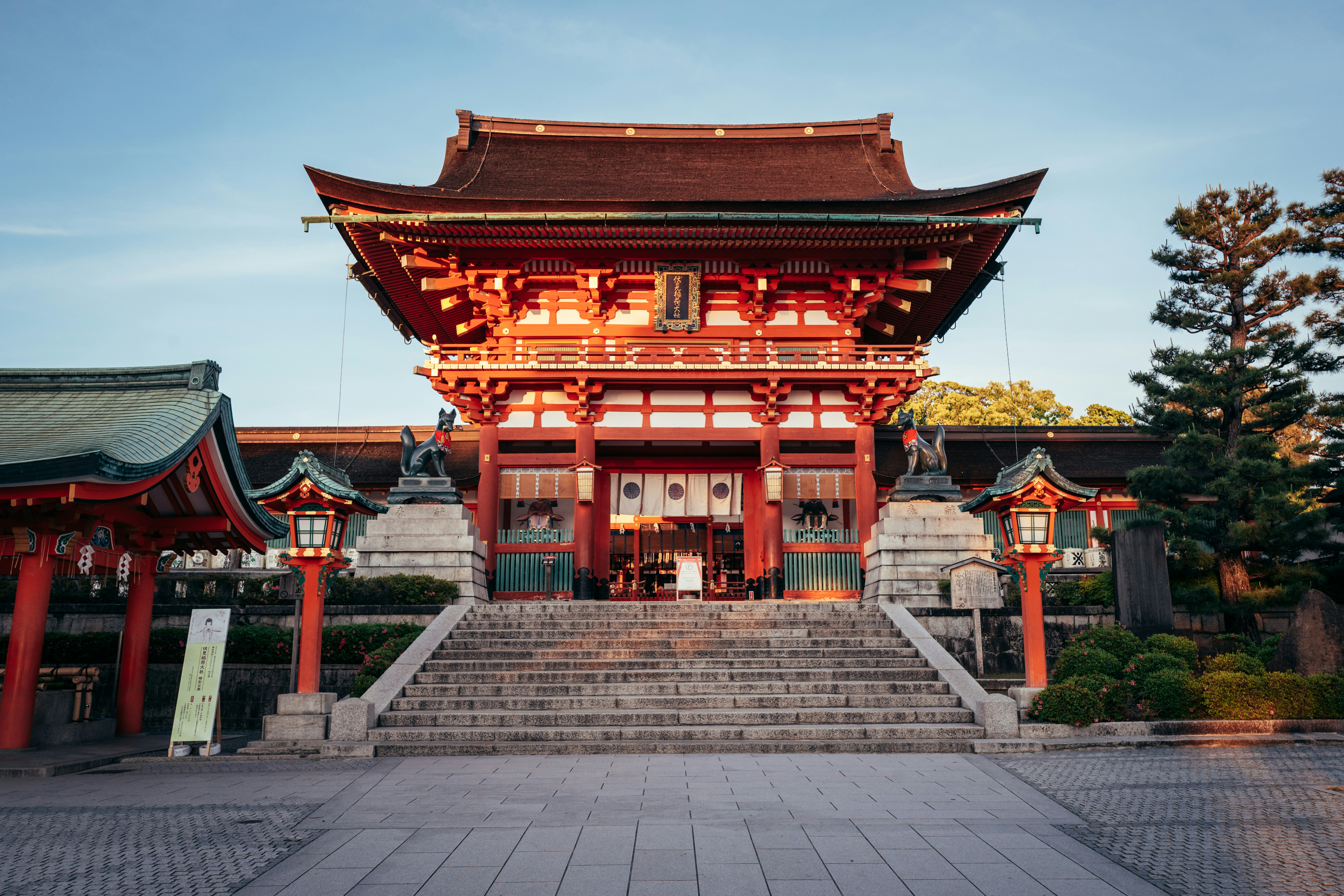 The magnificent Romon Gate of Fushimi Inari Taisha in Kyoto illuminated by warm golden sunlight, guarded by traditional Kitsune statues.