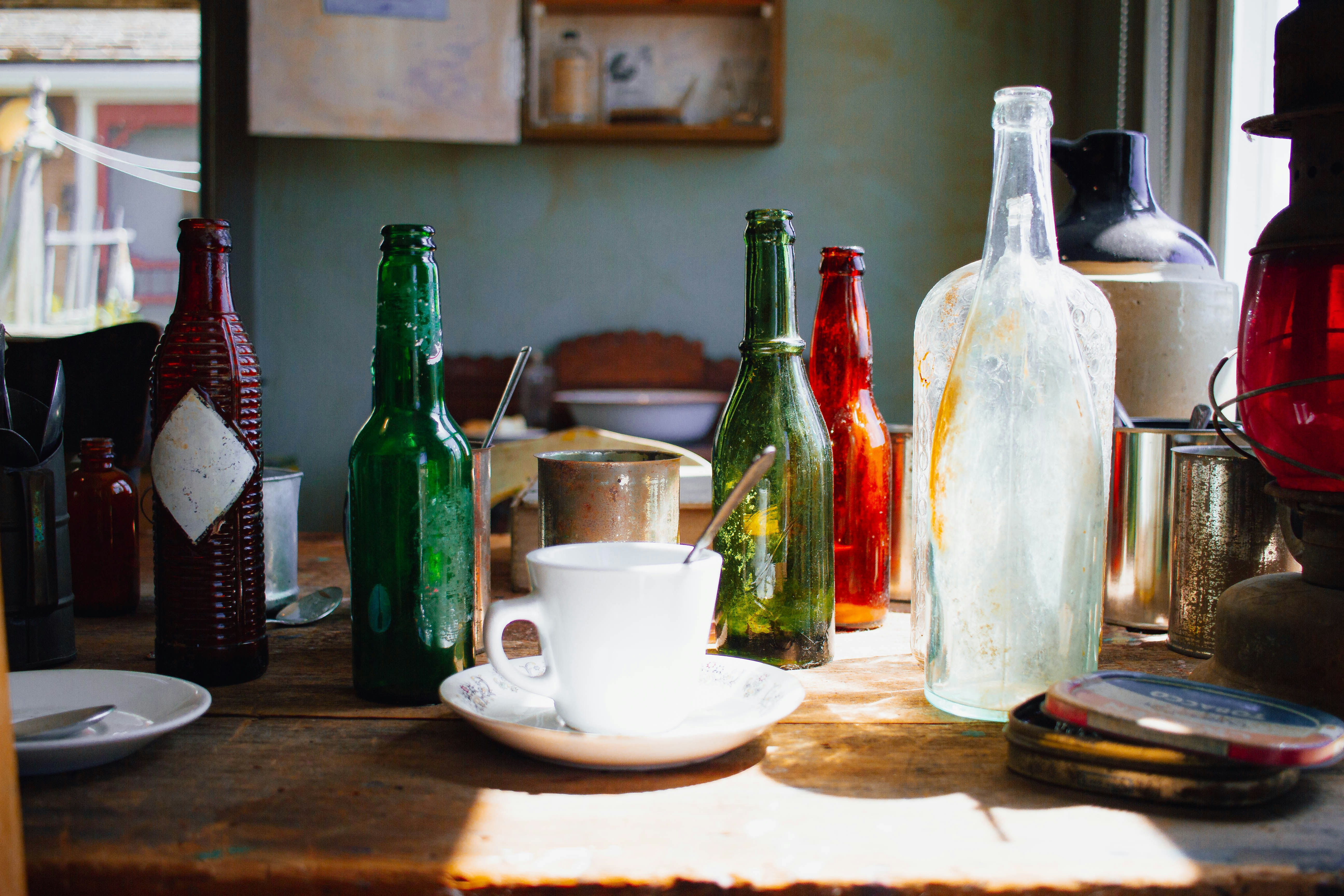 Sunlit Studio Still-Life: Glass Bottles and White Cup on a Weathered Table